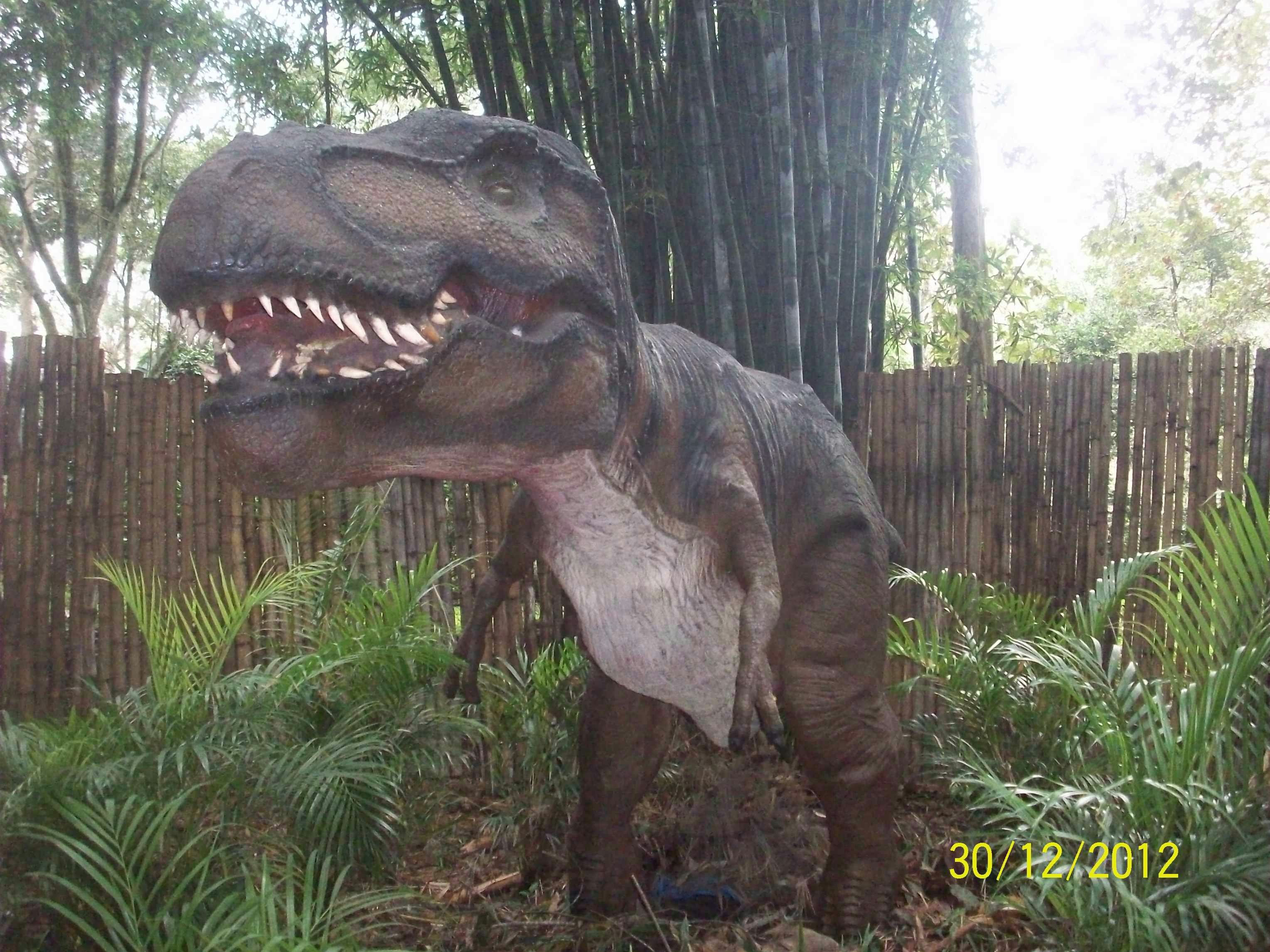 A large dinosaur statue stands among green foliage and bamboo.