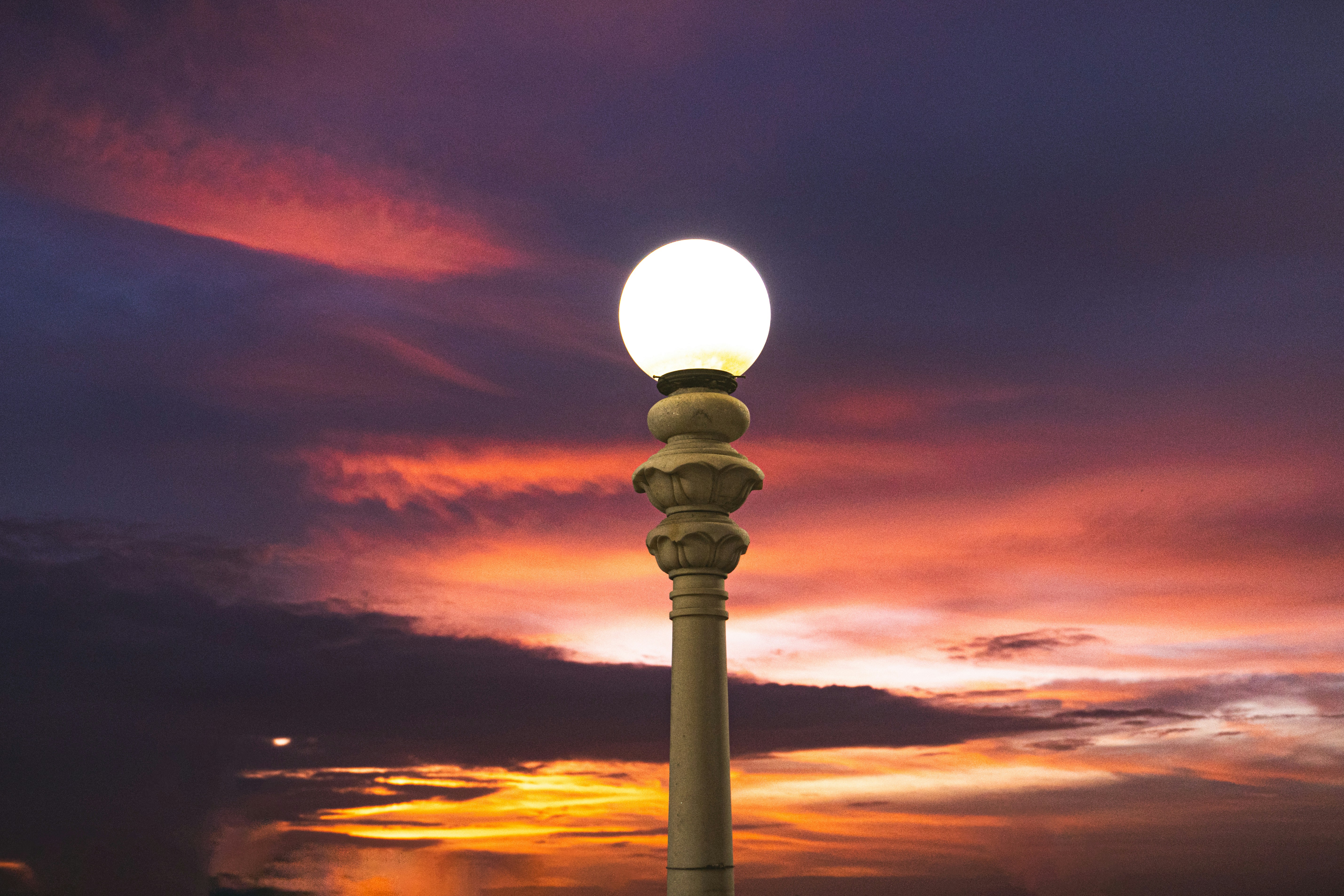 Glowing Orb atop a Sculpted Lamp Against a Fiery Sunset