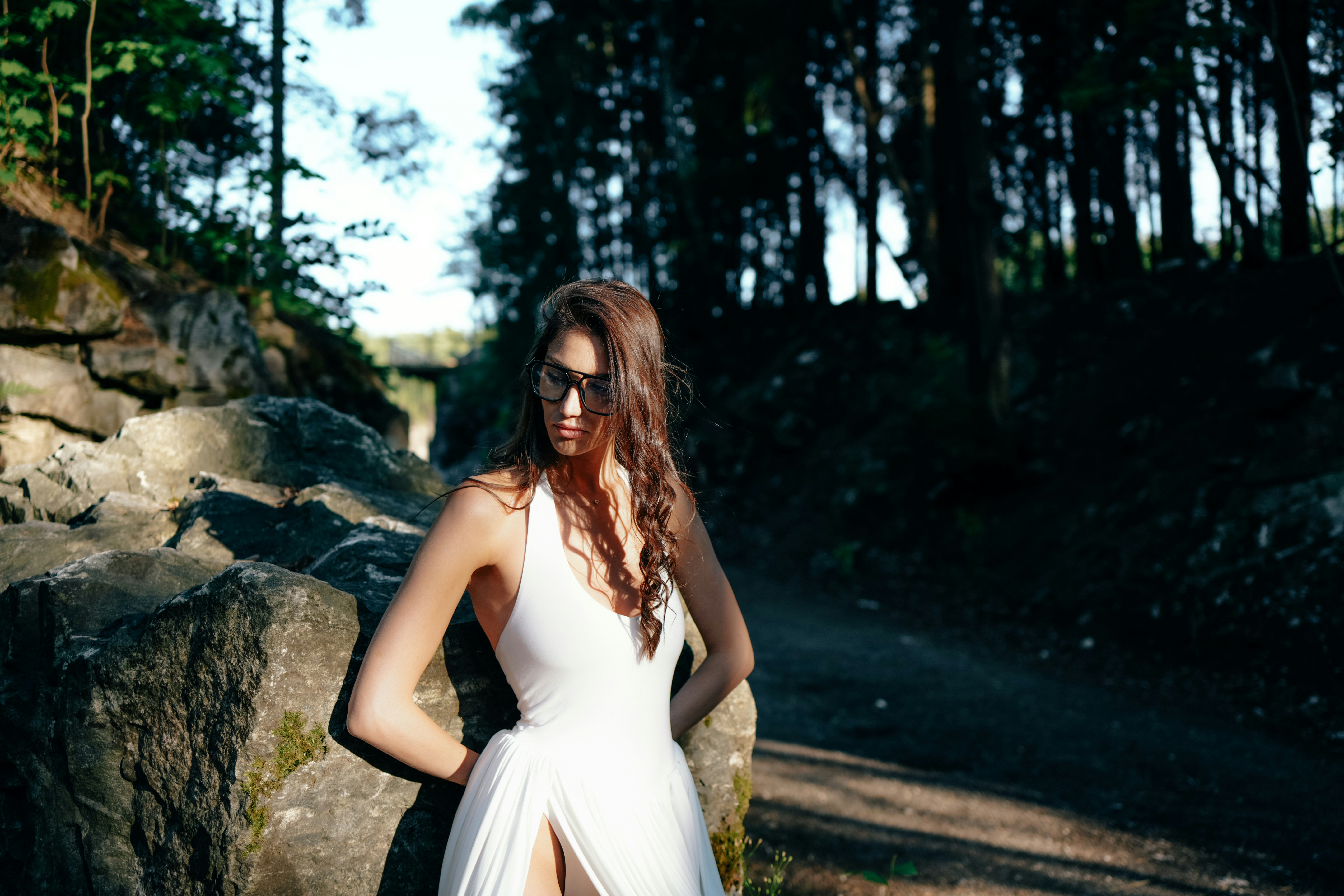 White dress, dark woods: a portrait against sunlit stone