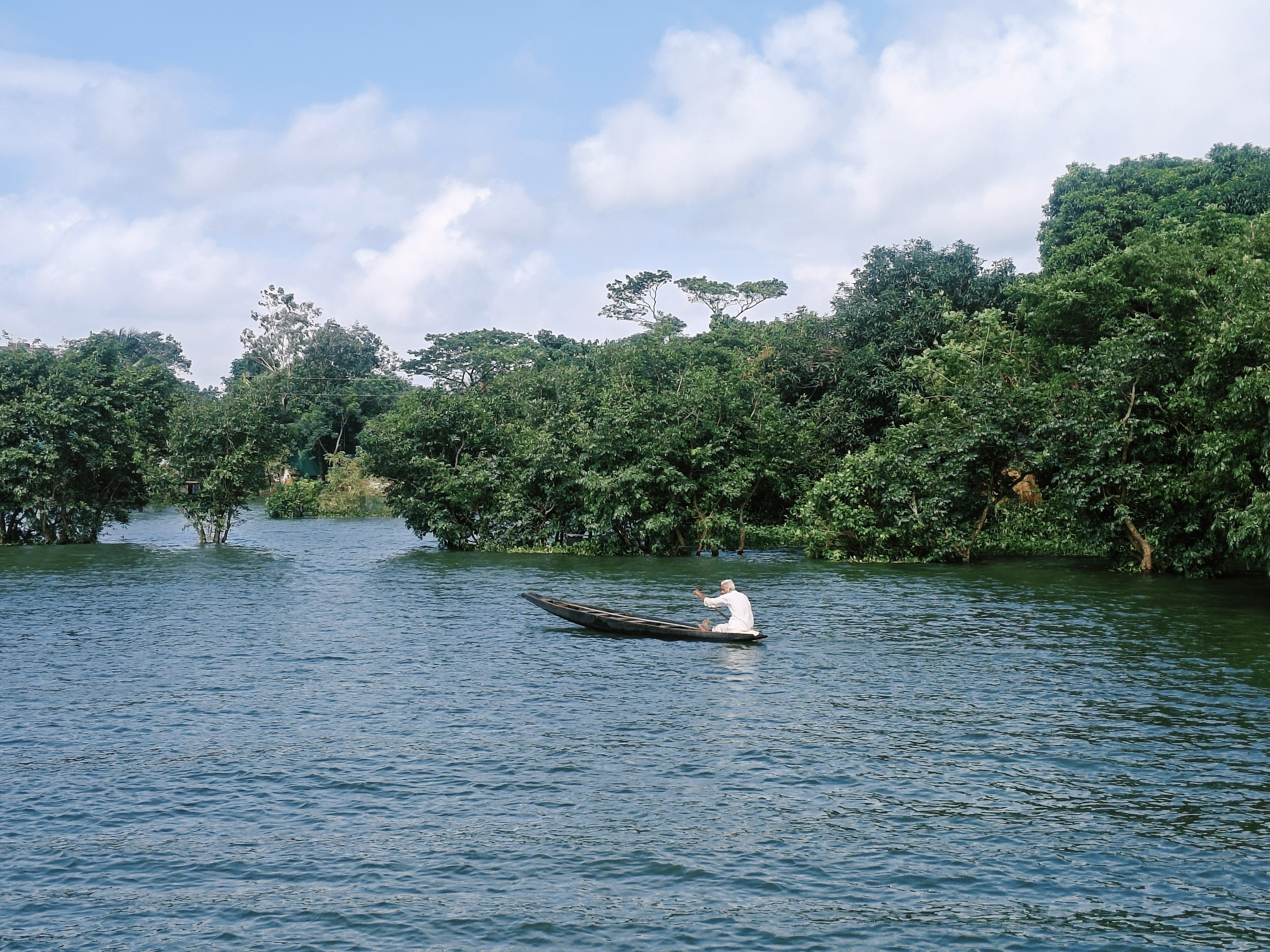 A solitary boatman rowing a traditional wooden boat through vibrant, clear waters surrounded by a dense flooded forest.