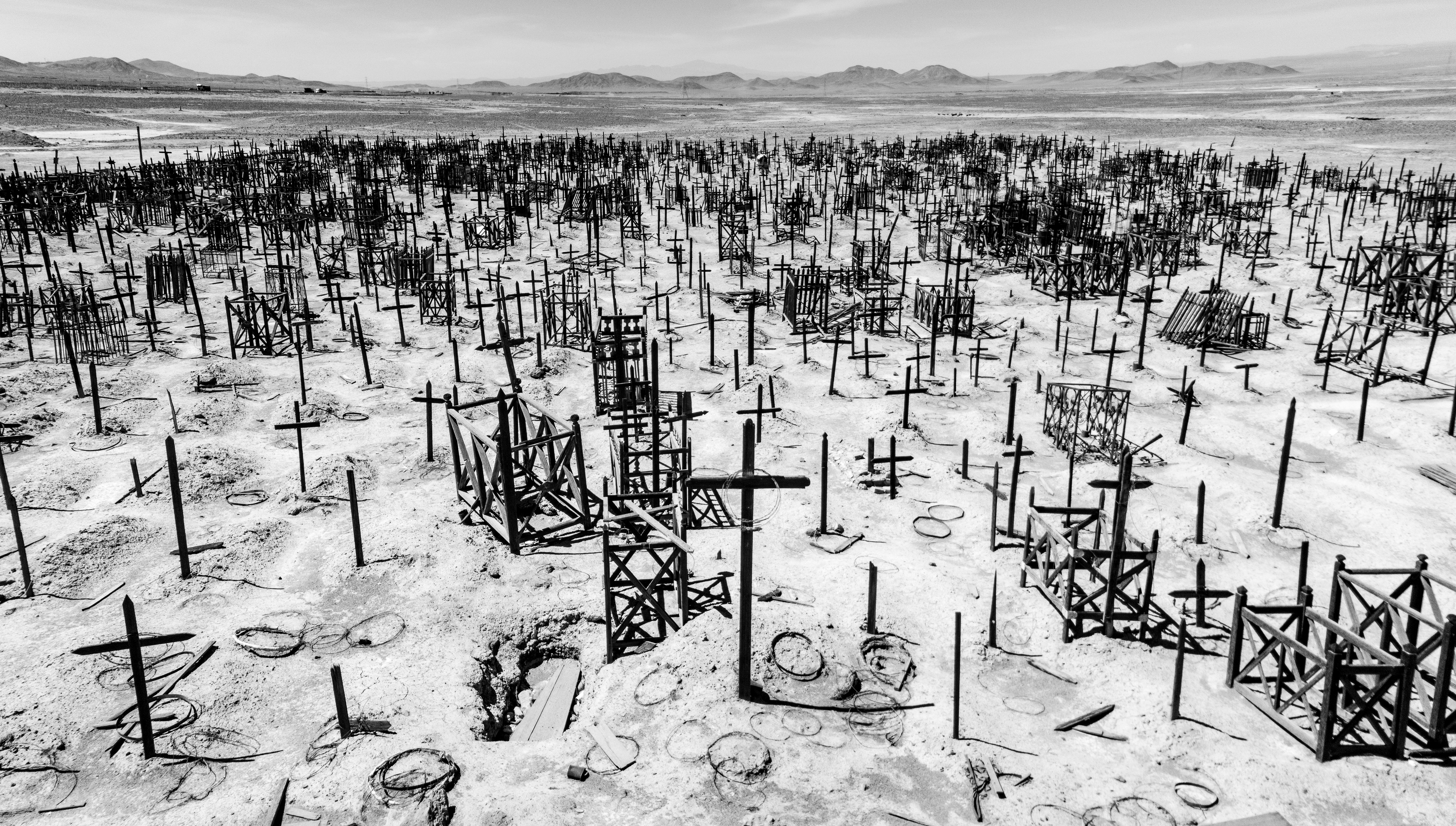 Monochrome construction yard remains speckle a barren landscape, with scattered wooden scaffolds and circular footprints stretching toward distant hills.