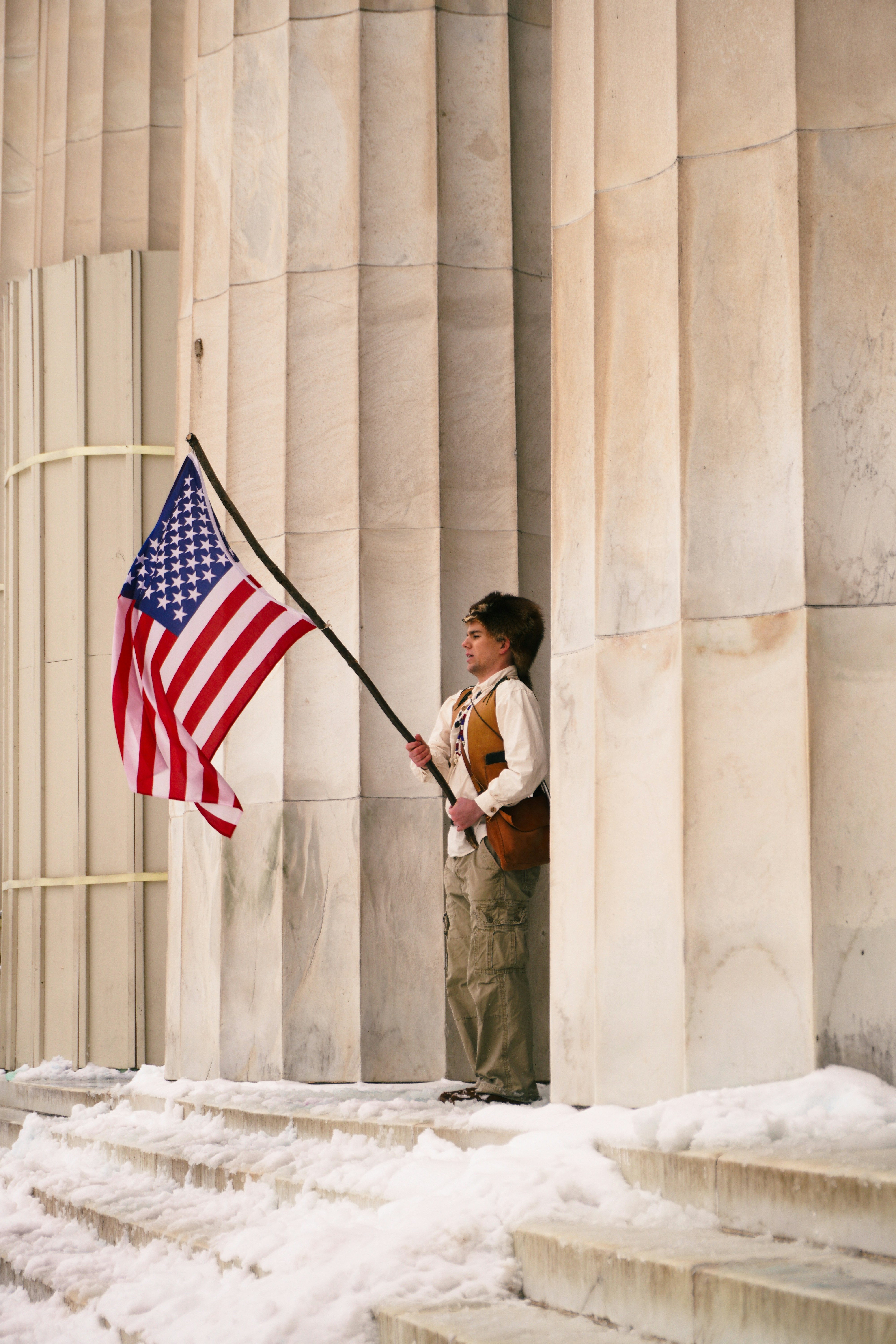 A man between the pillars of the Lincoln Memorial holds an American flag during Winter Storm Blair.