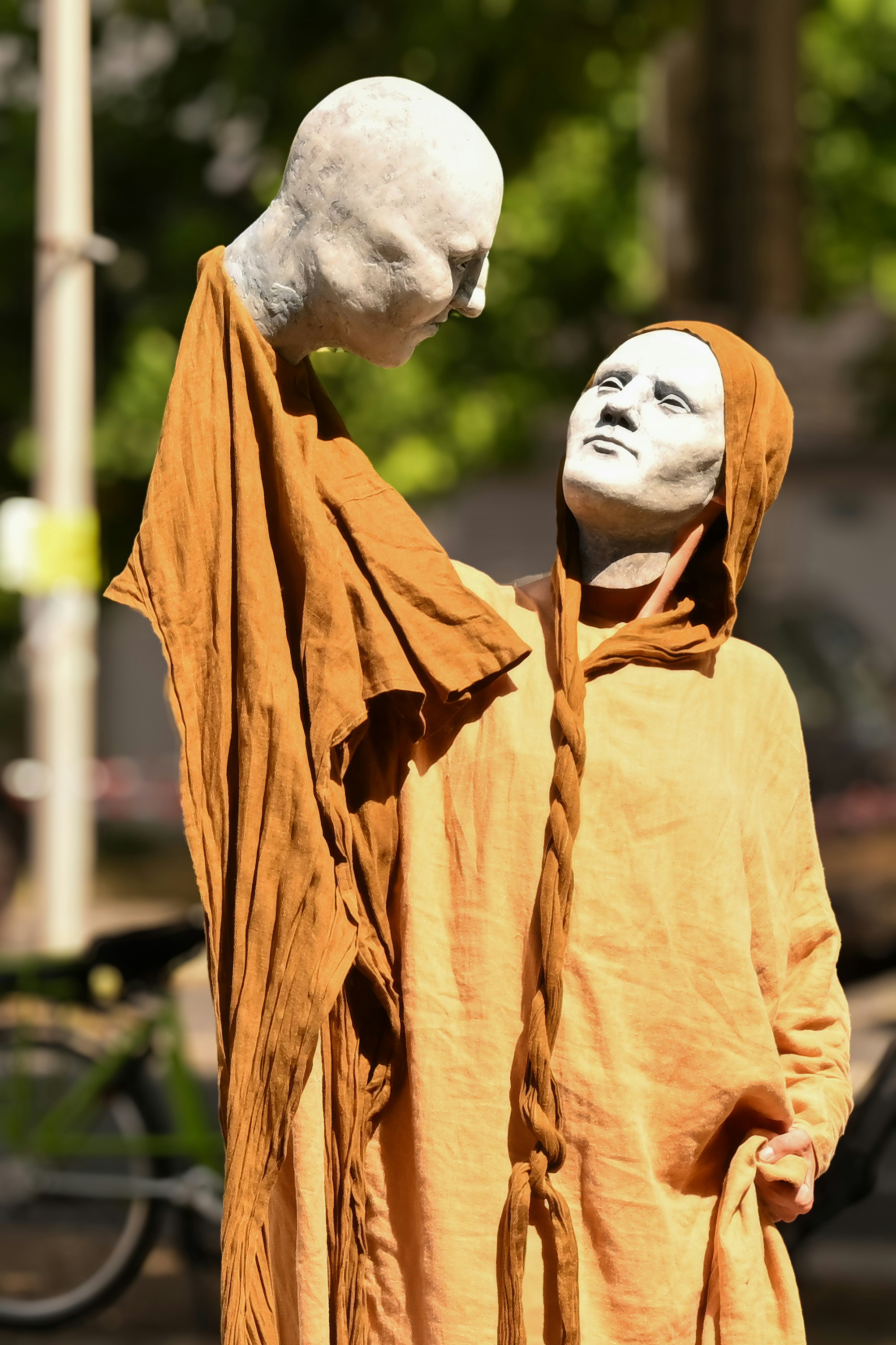 Two Masked Figures in Warm Orange Drapery Share a Silent Exchange