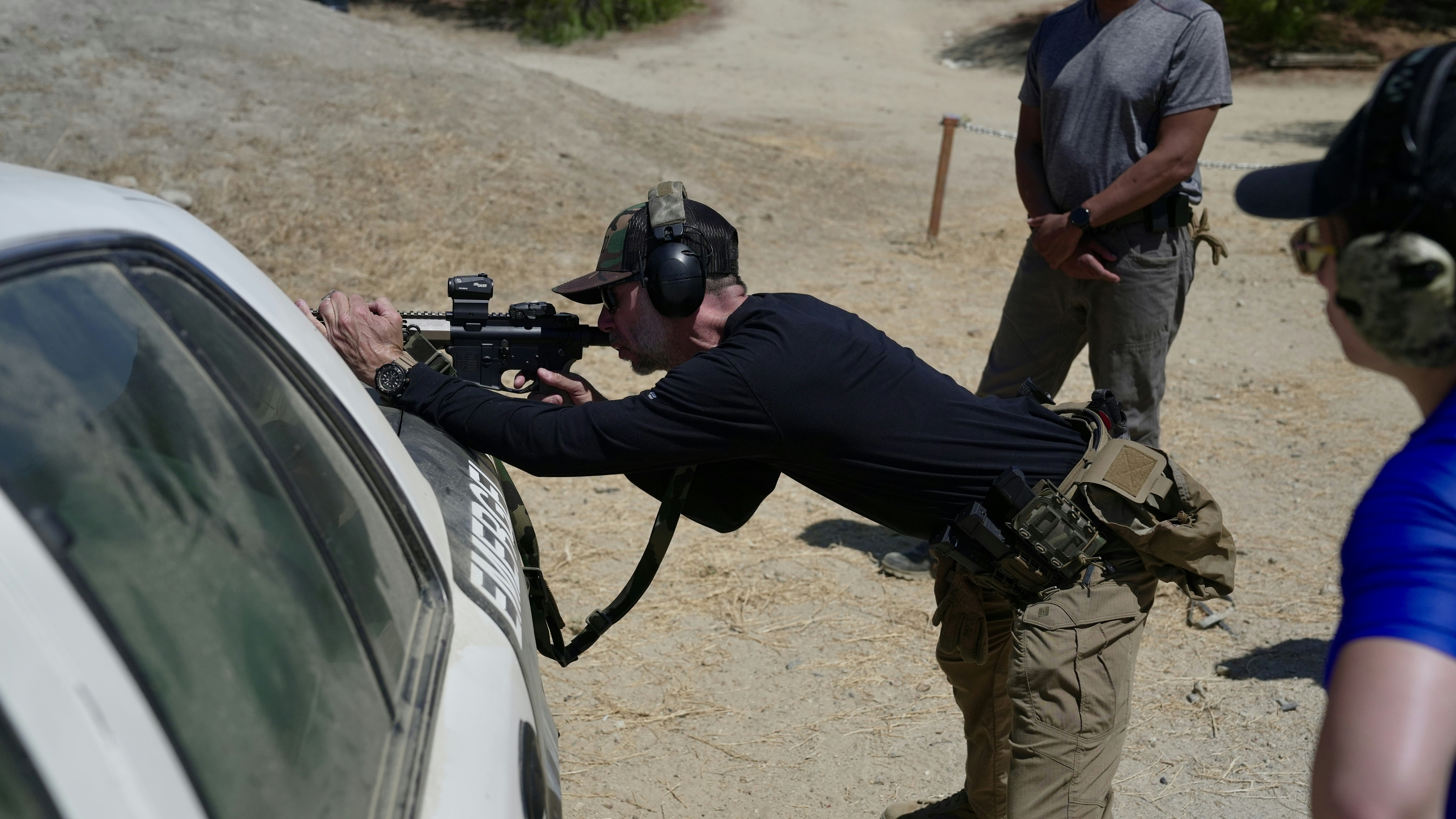 Aim and Ground: A prone shooter steadies his rifle beside the patrol car