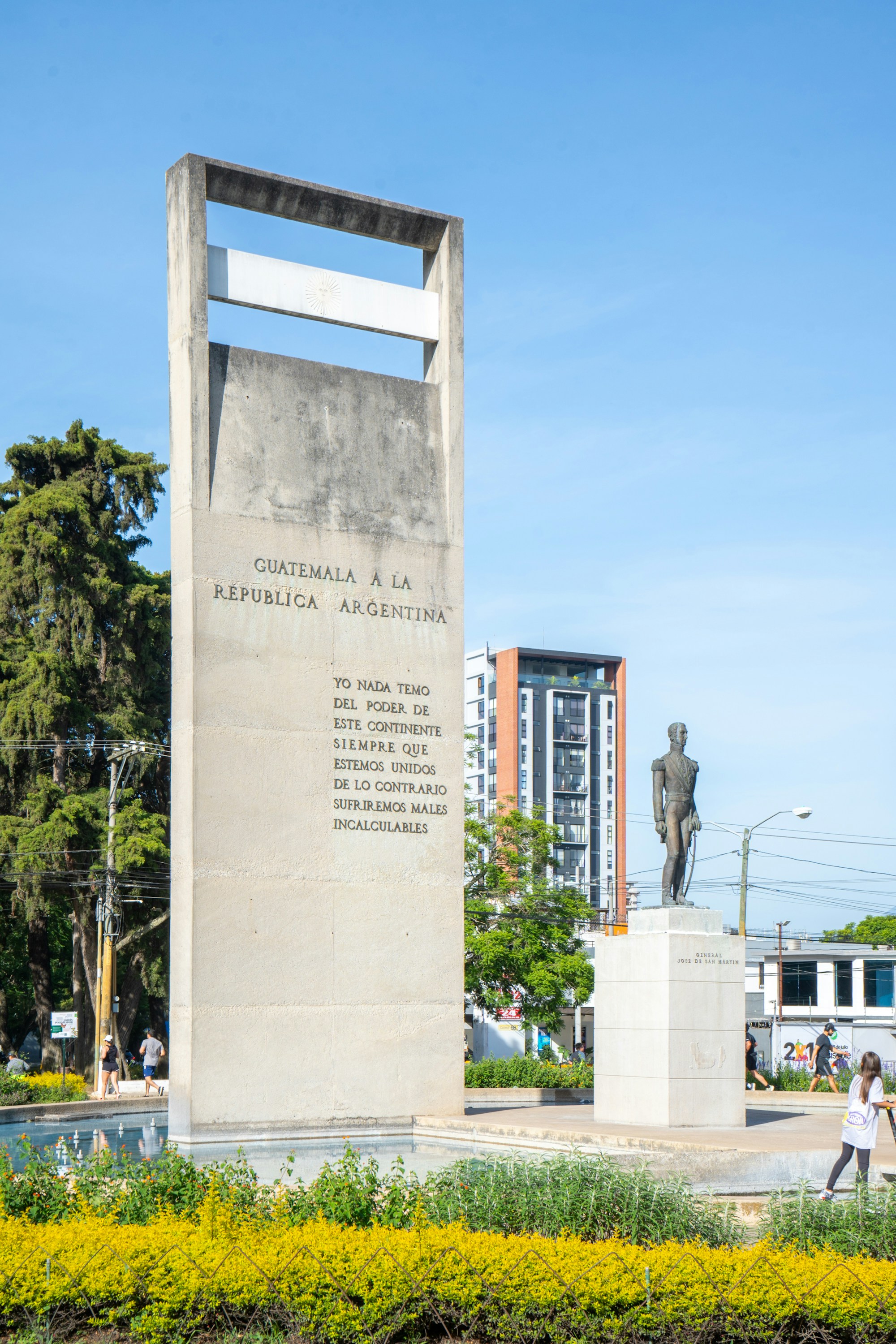 Monumental Axis: Concrete Pillars and a Distant Statue in a Sunlit Plaza