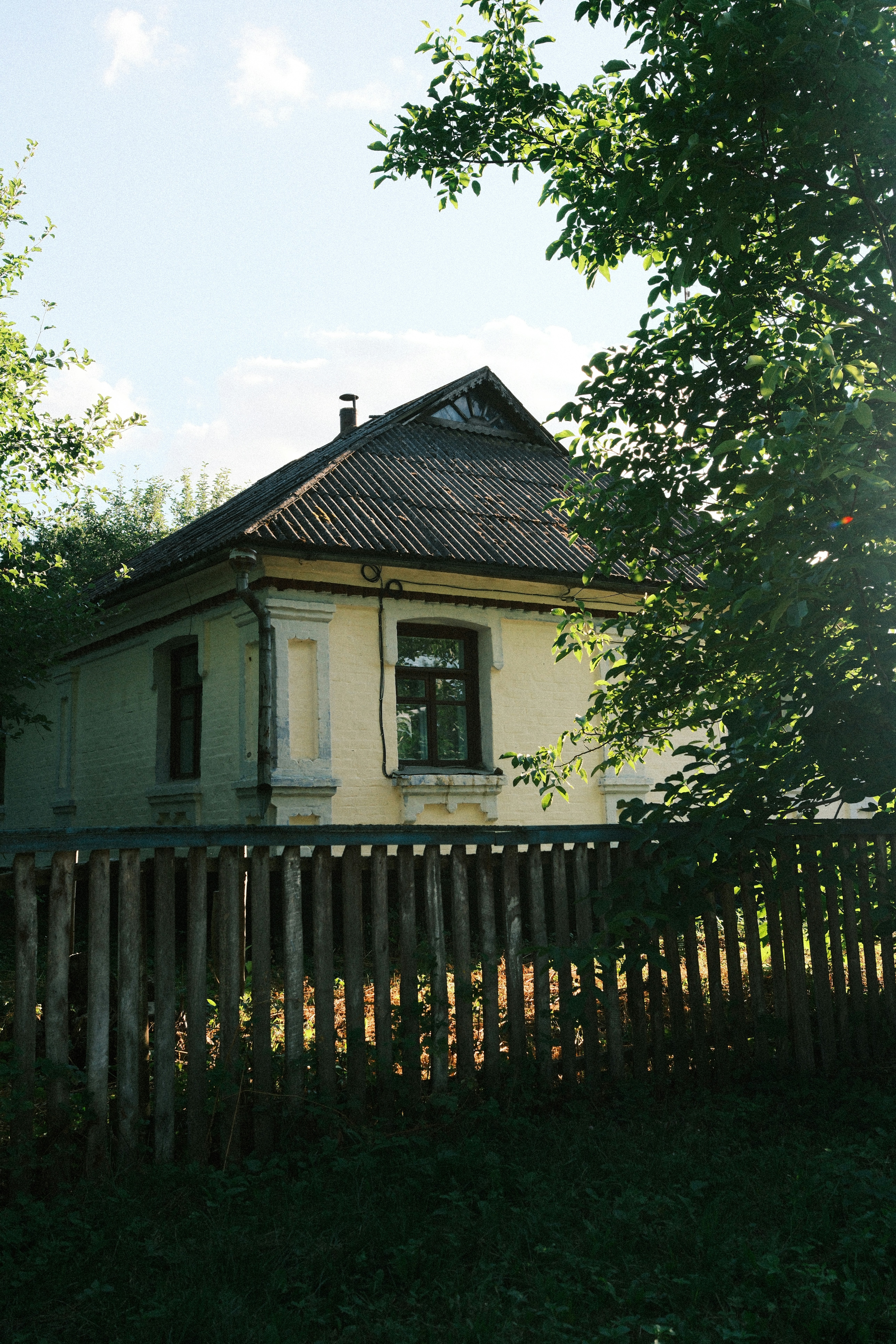 Old House Behind a Slatted Fence Under a Sunlit Canopy
