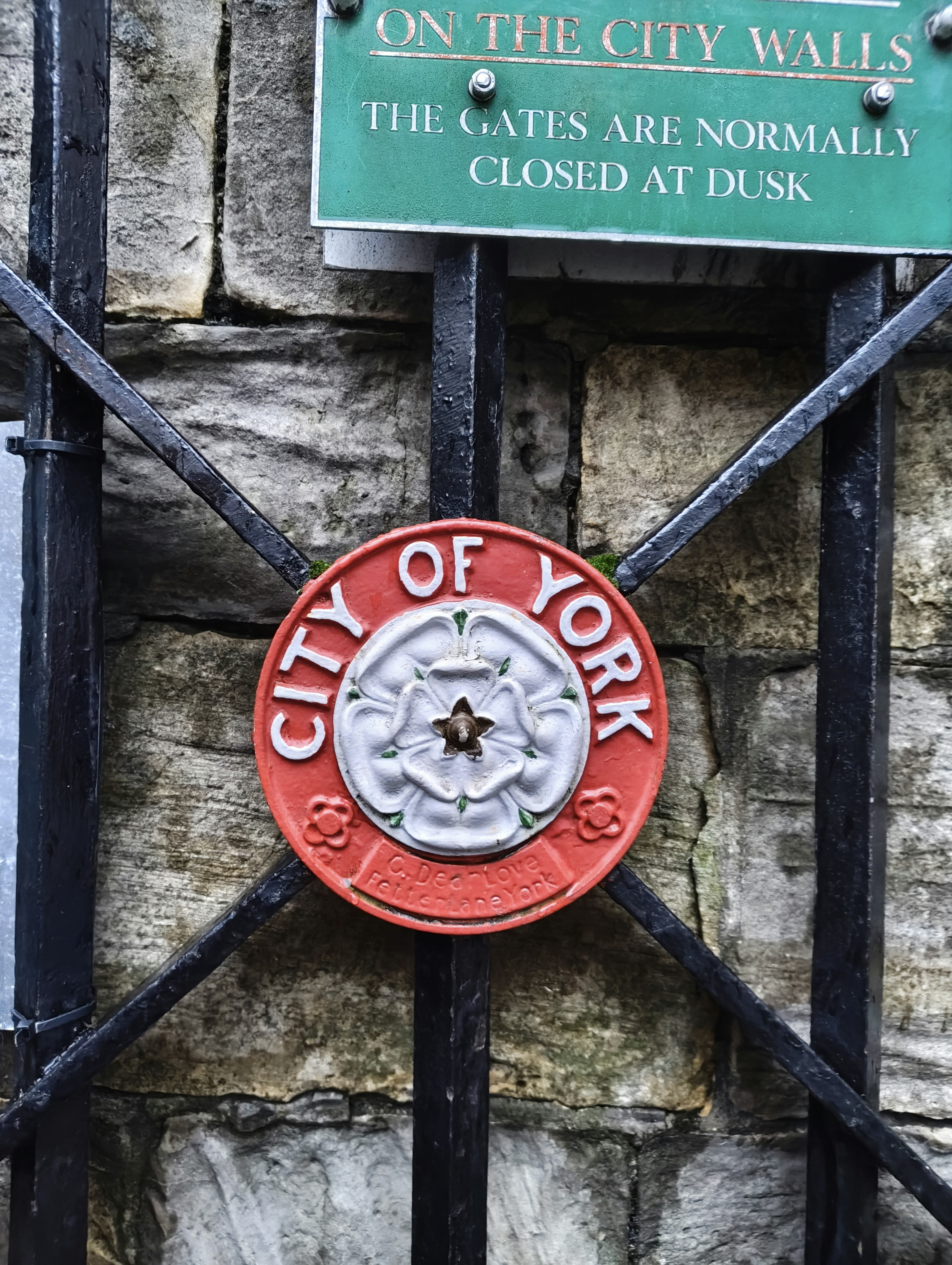 Close-up of a red circular City of York emblem mounted on a black iron grate with stone wall in the background.