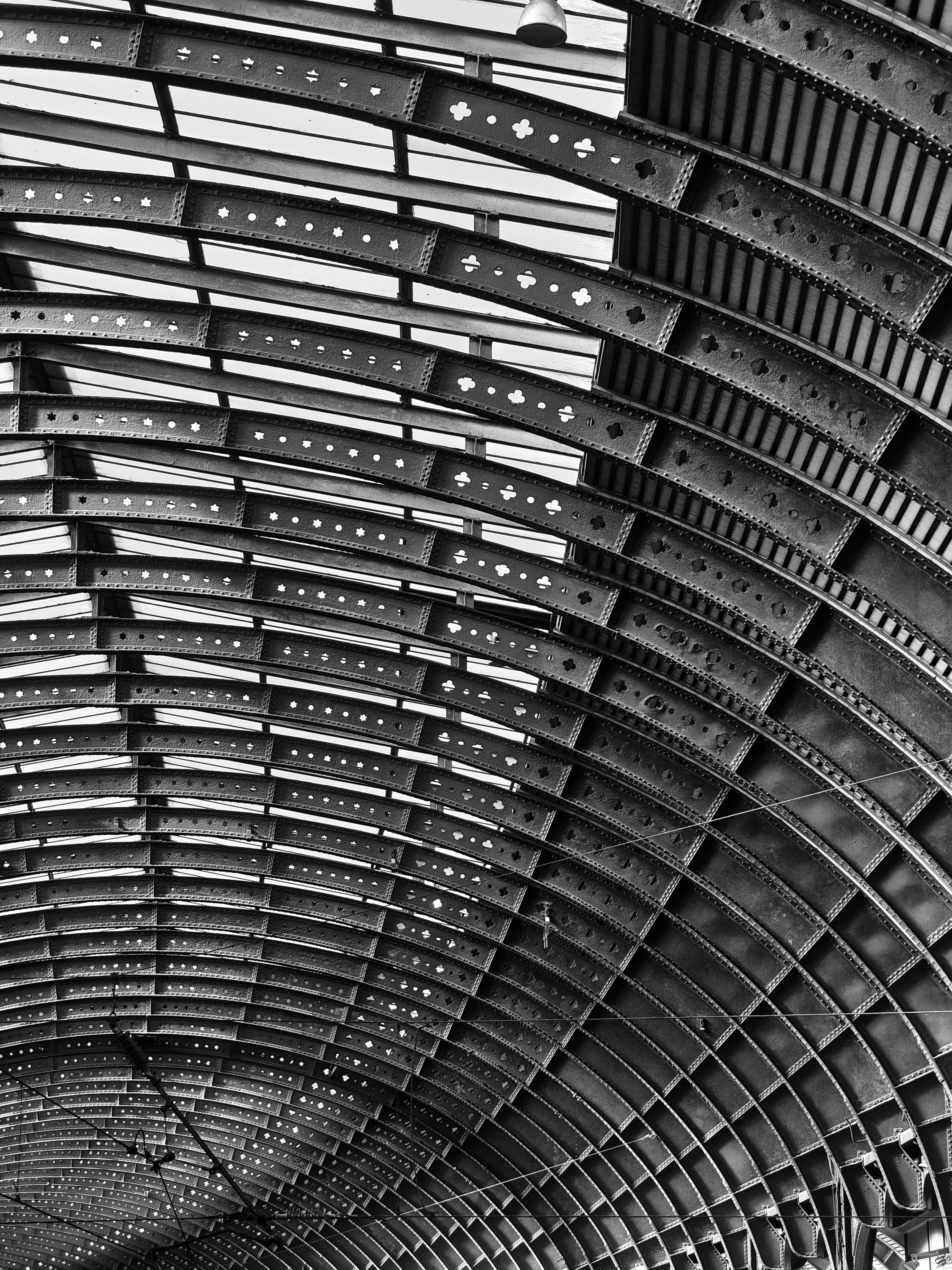 Dramatic monochrome close-up of a metal spiral structure with repeating radial rings and riveted segments forming a tunnel-like pattern.