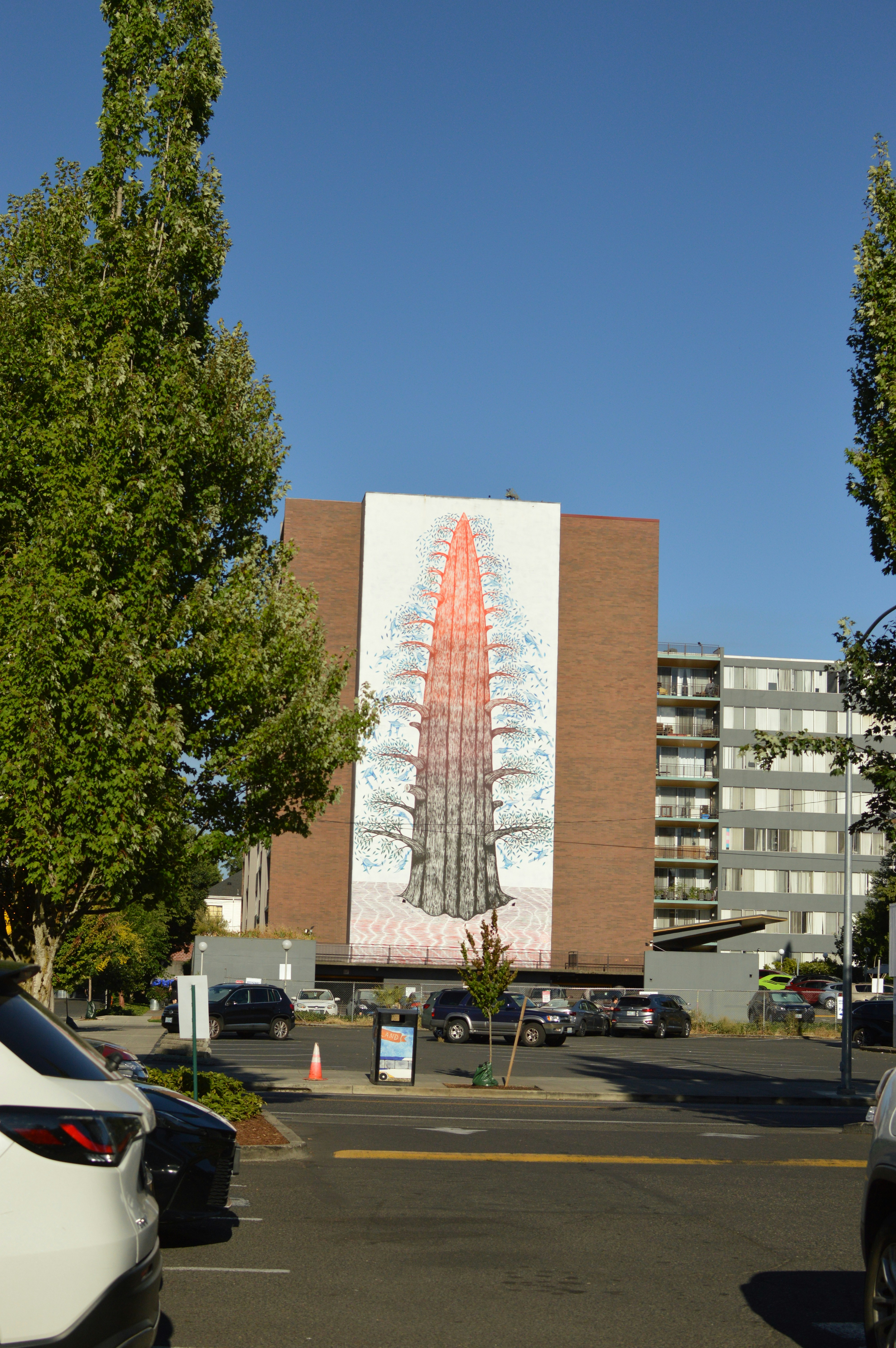 Vertical mural on brick building framed by trees in a parking lot