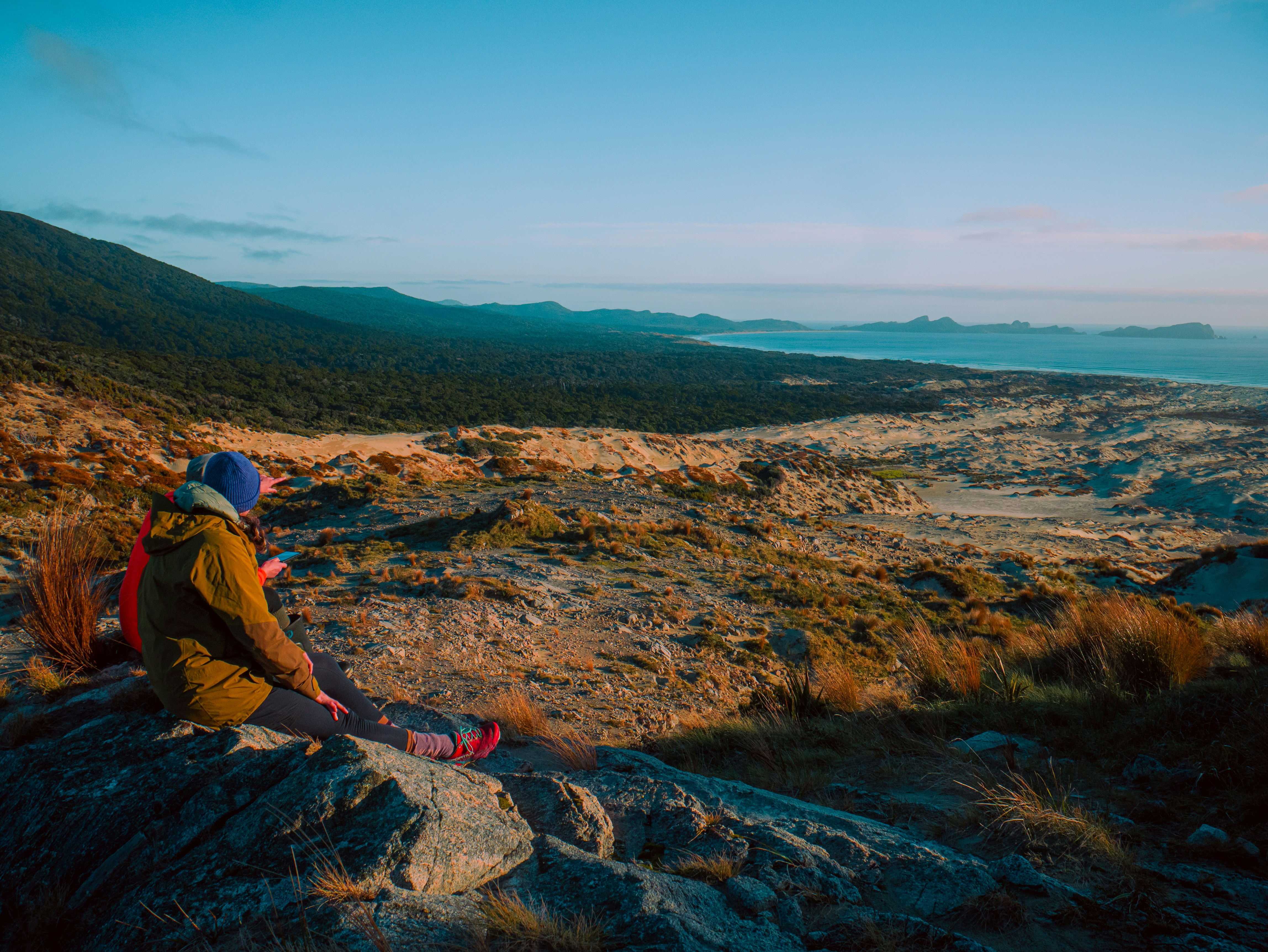 Sunlit cliffside rest: a hiker gazes toward a distant coastline
