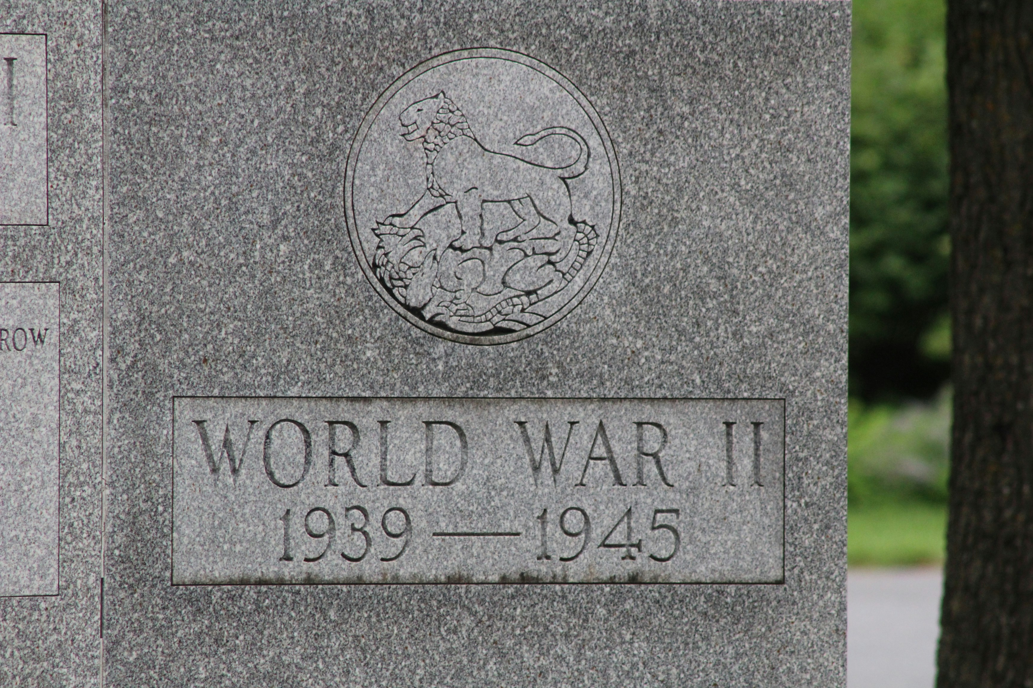 Granite memorial plaque with World War II inscription and circular emblem; the composition centers on the engraved text and emblem, suggesting a commemorative monument context.