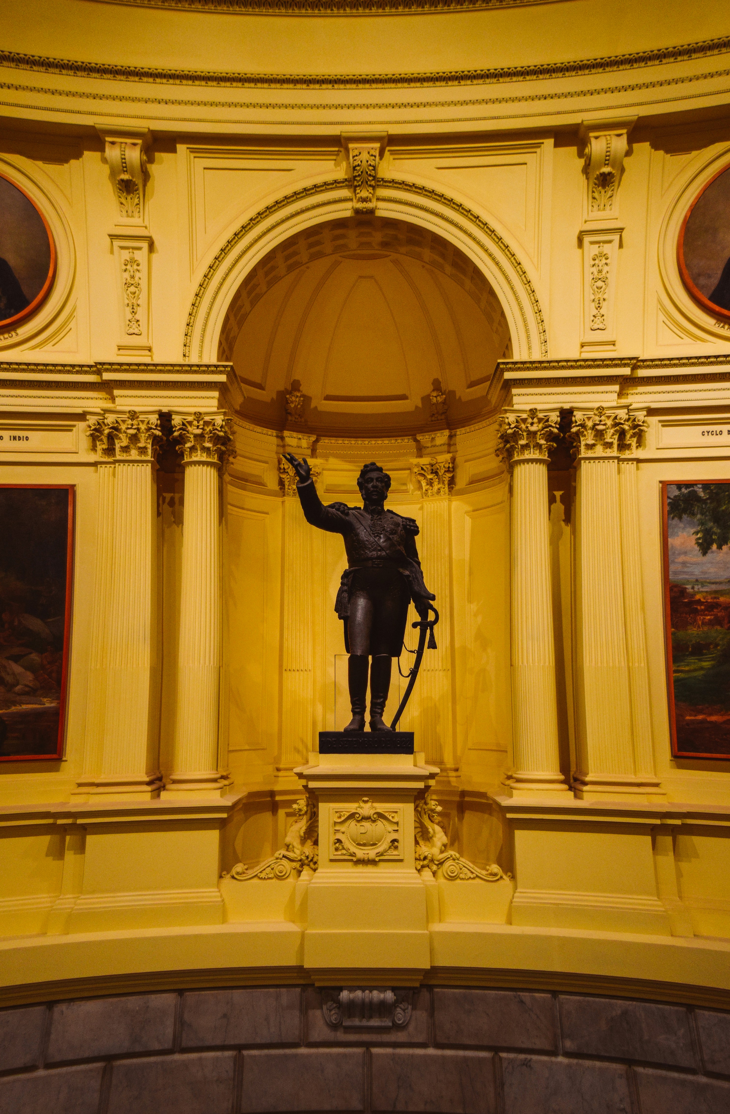 Statue of a sword-wielding figure framed by ornate neoclassical archways inside a yellow-toned hall