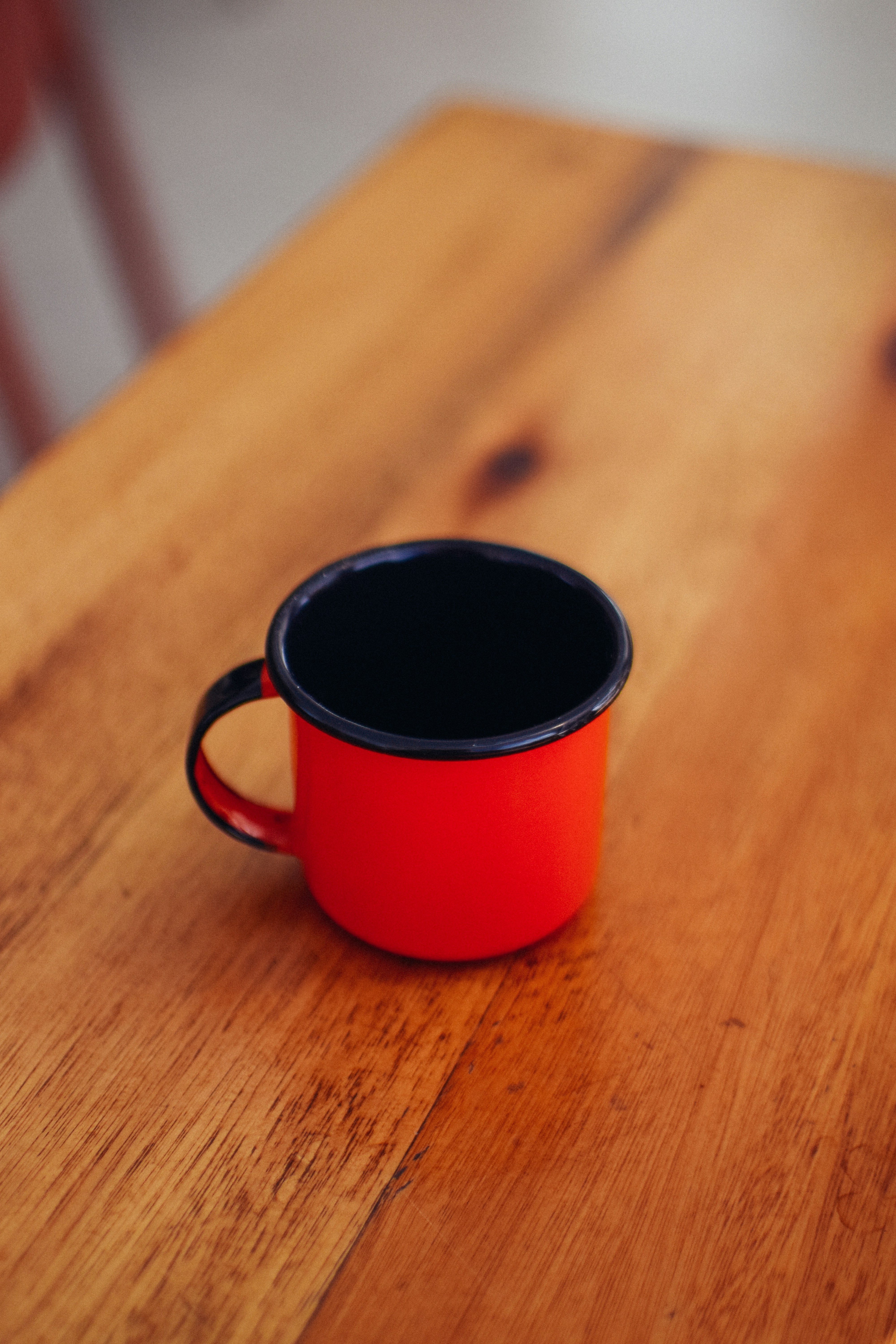 Bright red coffee mug sits on a wooden table, foreground focus with a soft blurred background; a simple still-life emphasizing color and texture. This is a product/photo study on natural light.