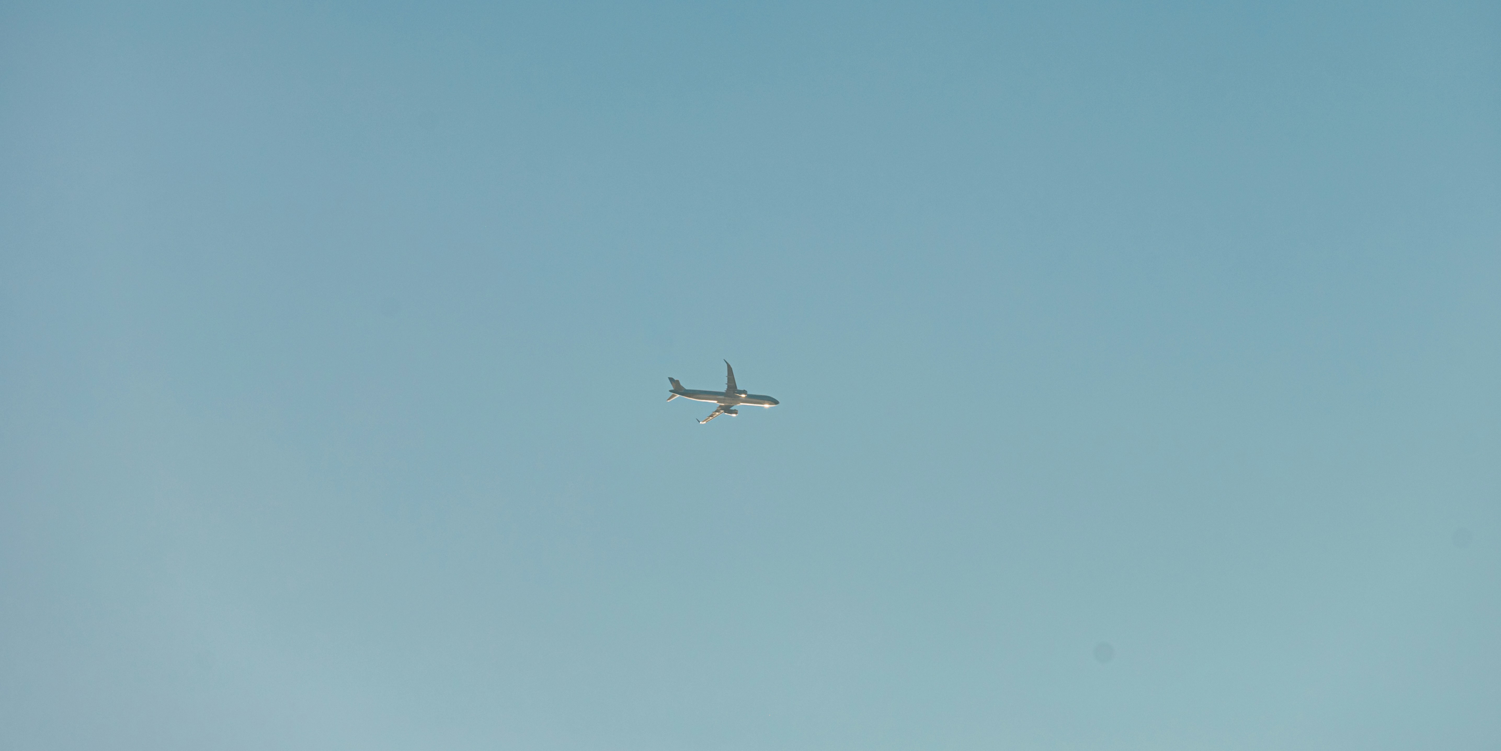 A lone jet traces a thin white line across a pale sky