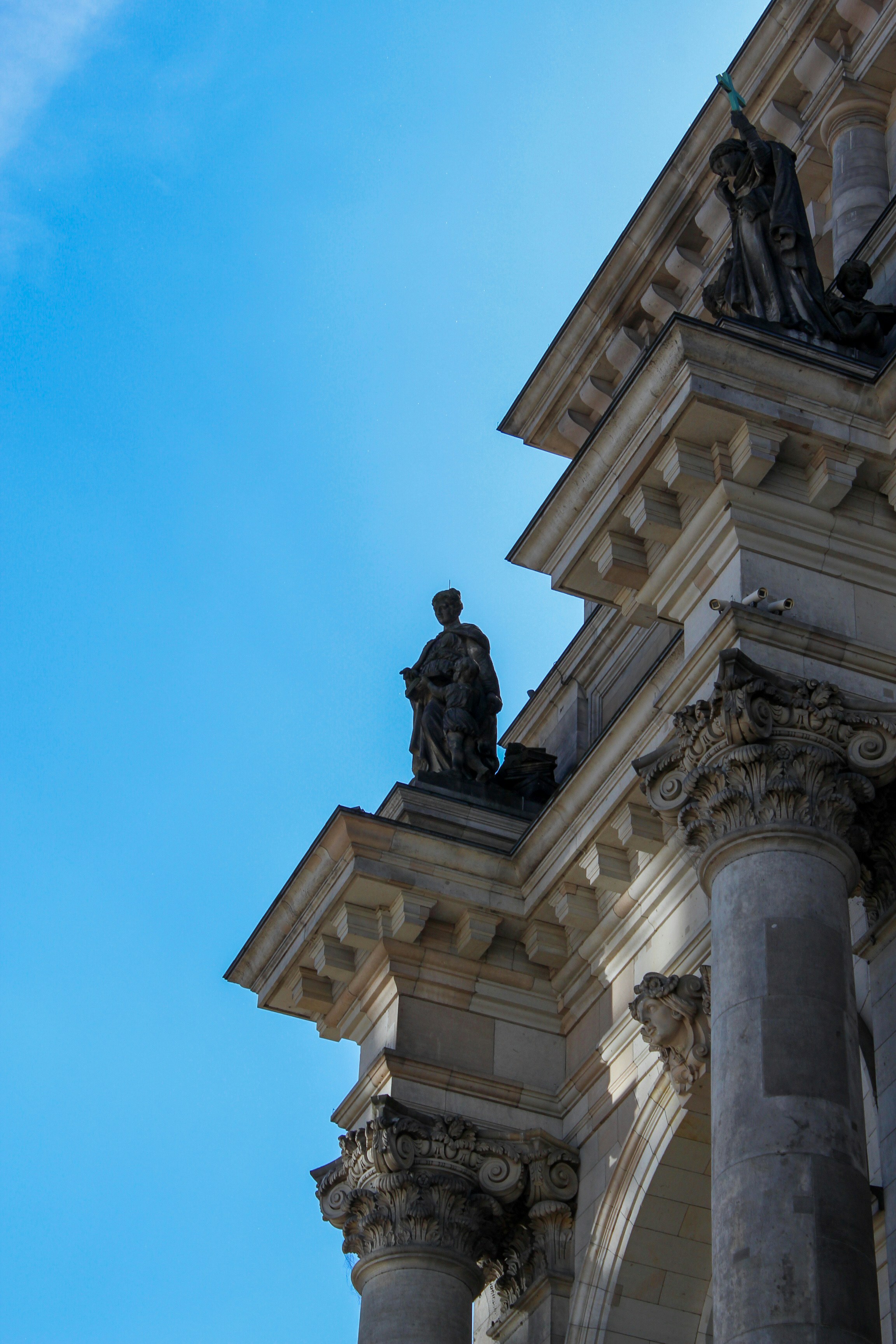 Architectural sculptures atop a classical façade with ornate columns under a bright blue sky.