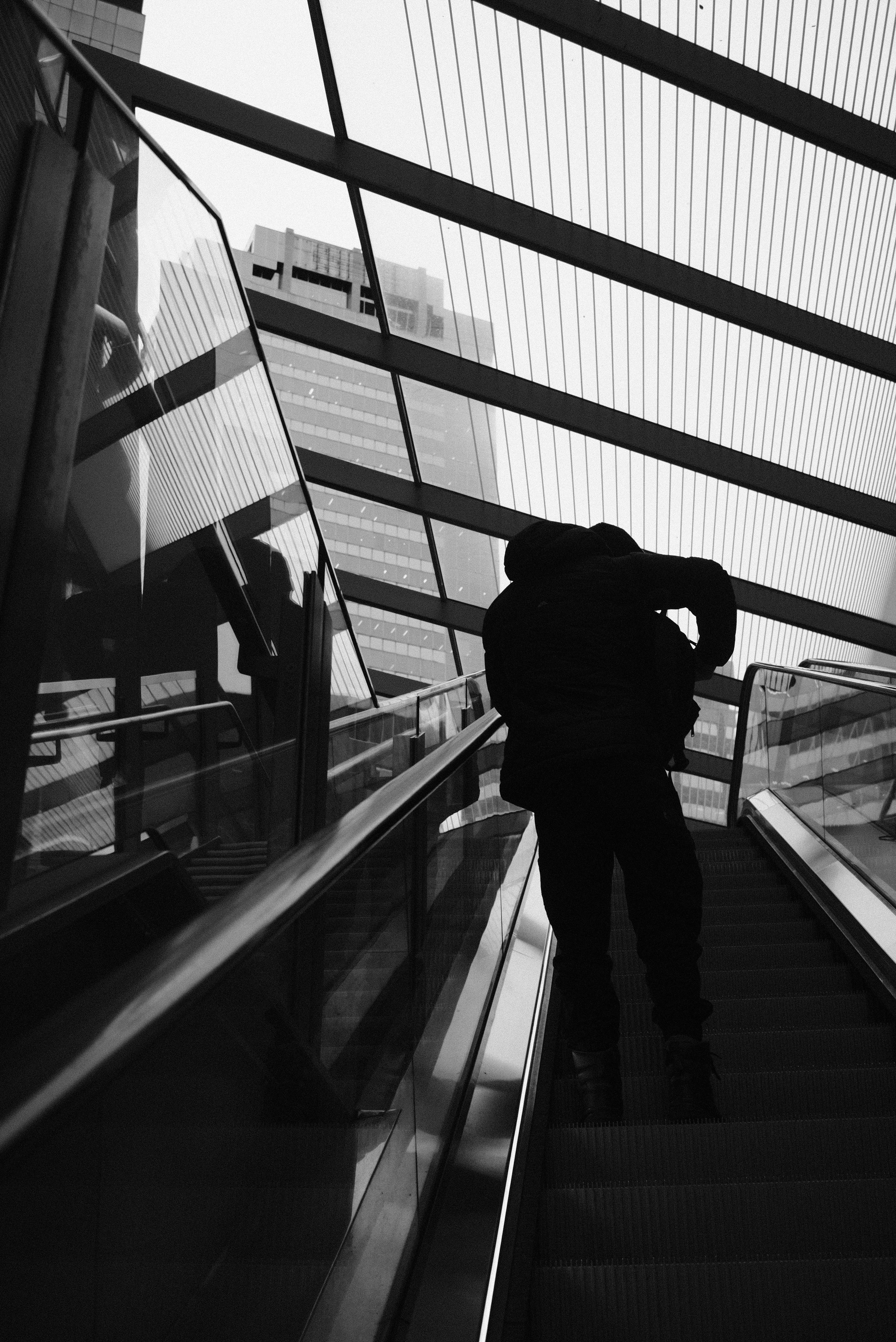 Striding Upward: A silhouette on the glass-edged escalator