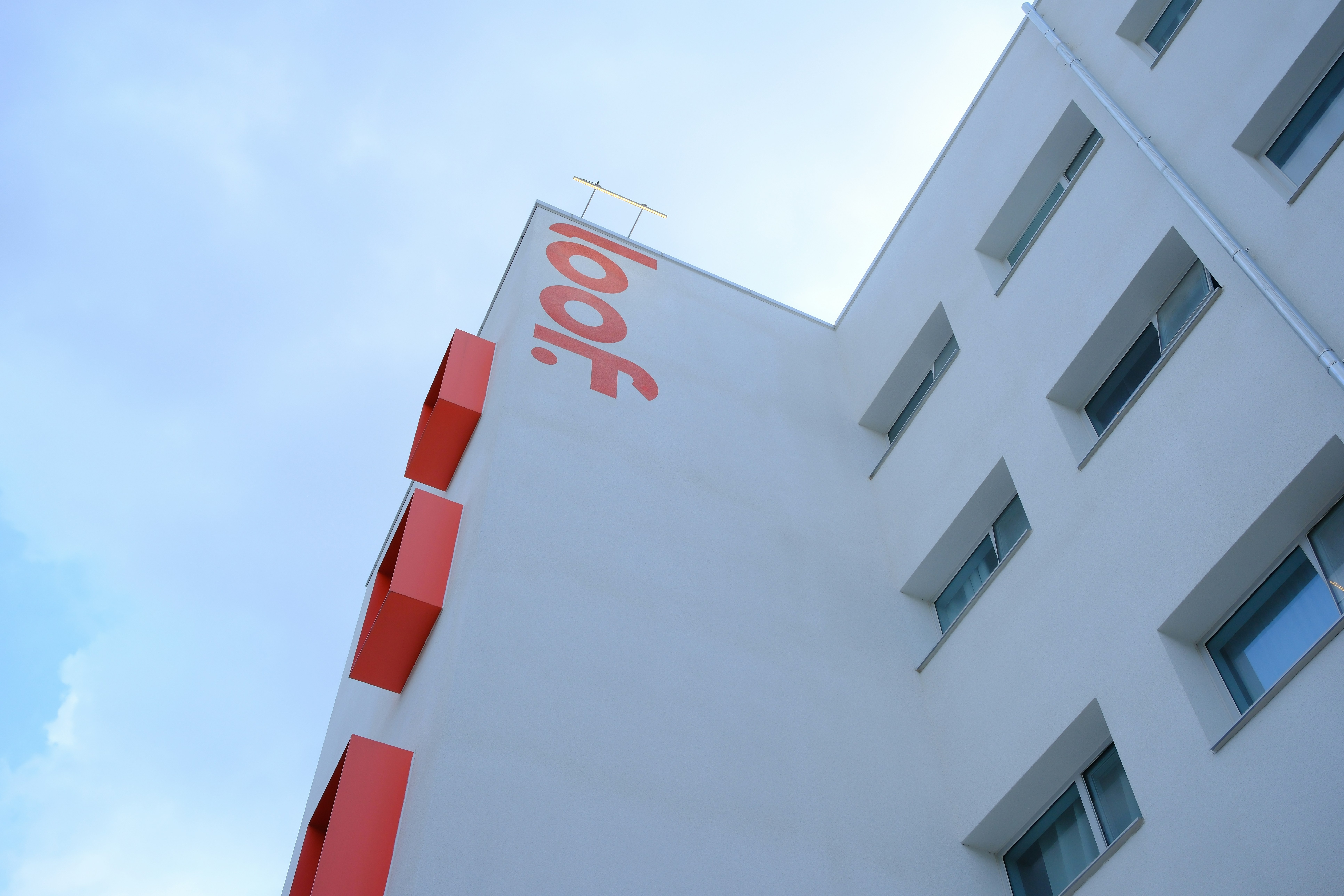 Red accents on a white apartment block reaching toward a blue sky