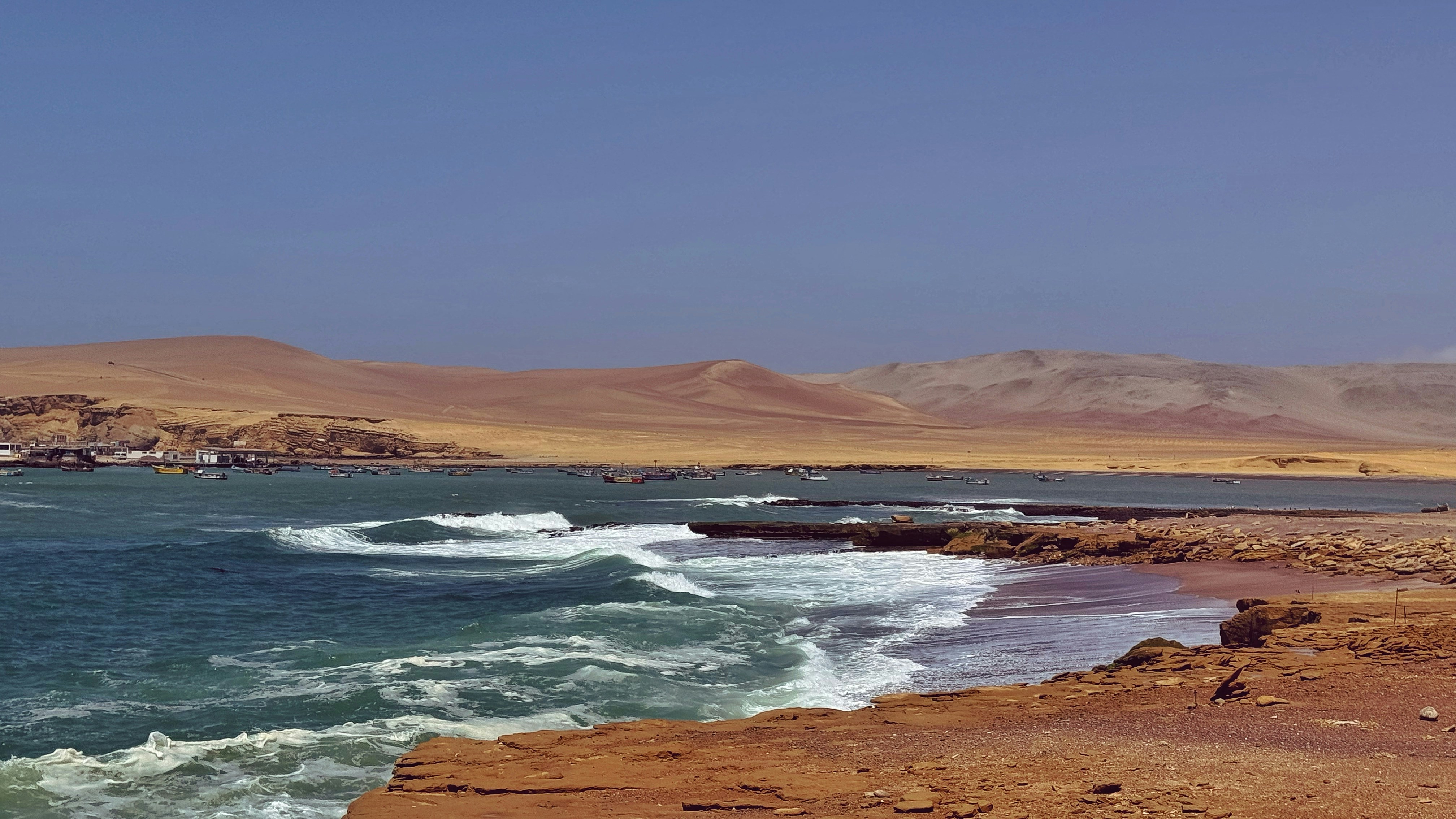 Deserted coastal horizon: waves kiss amber cliffs under a pale blue sky