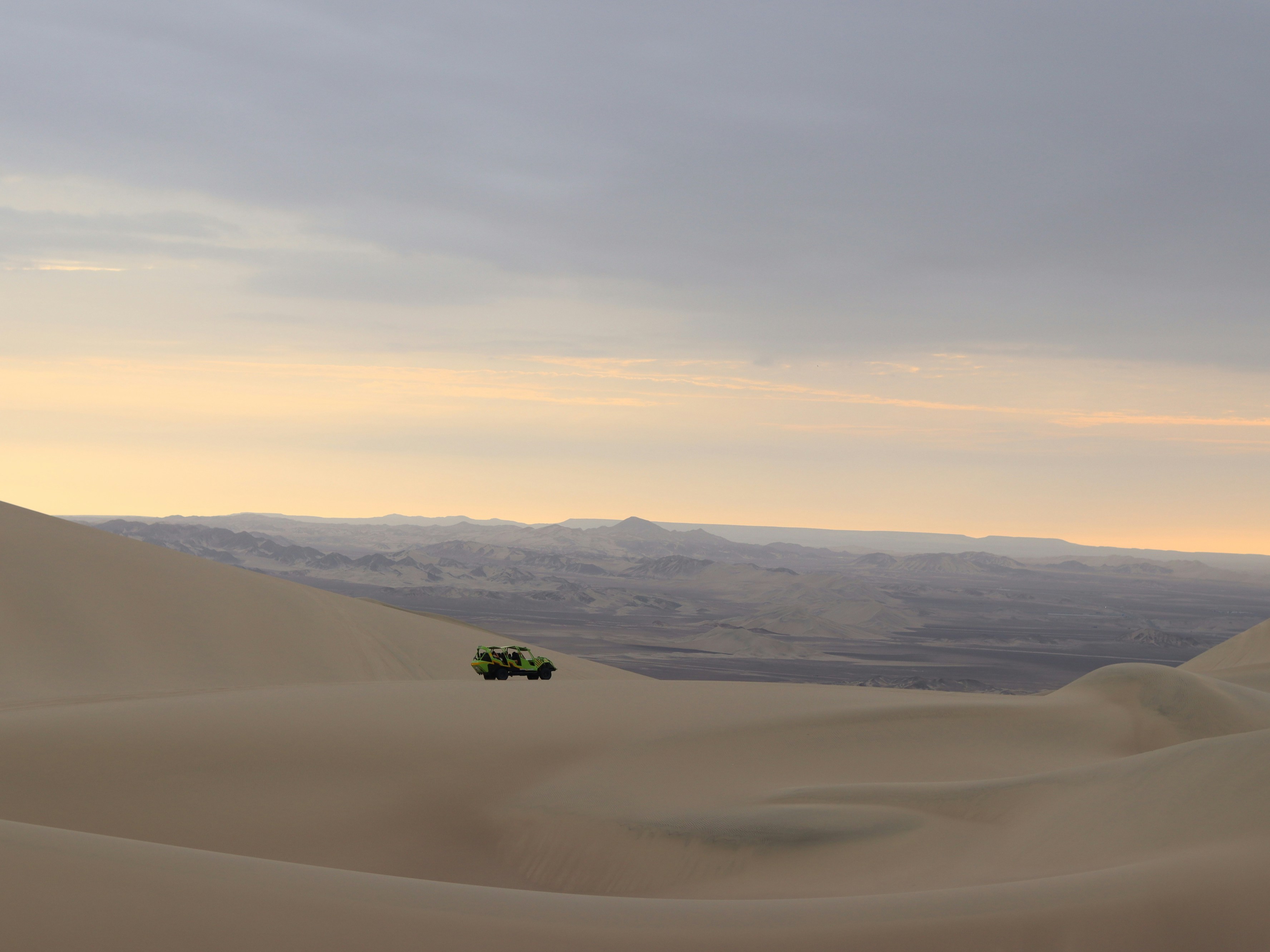 Desert Ridge: A Tiny Green Vehicle Amid Immense Dunes at Sunset