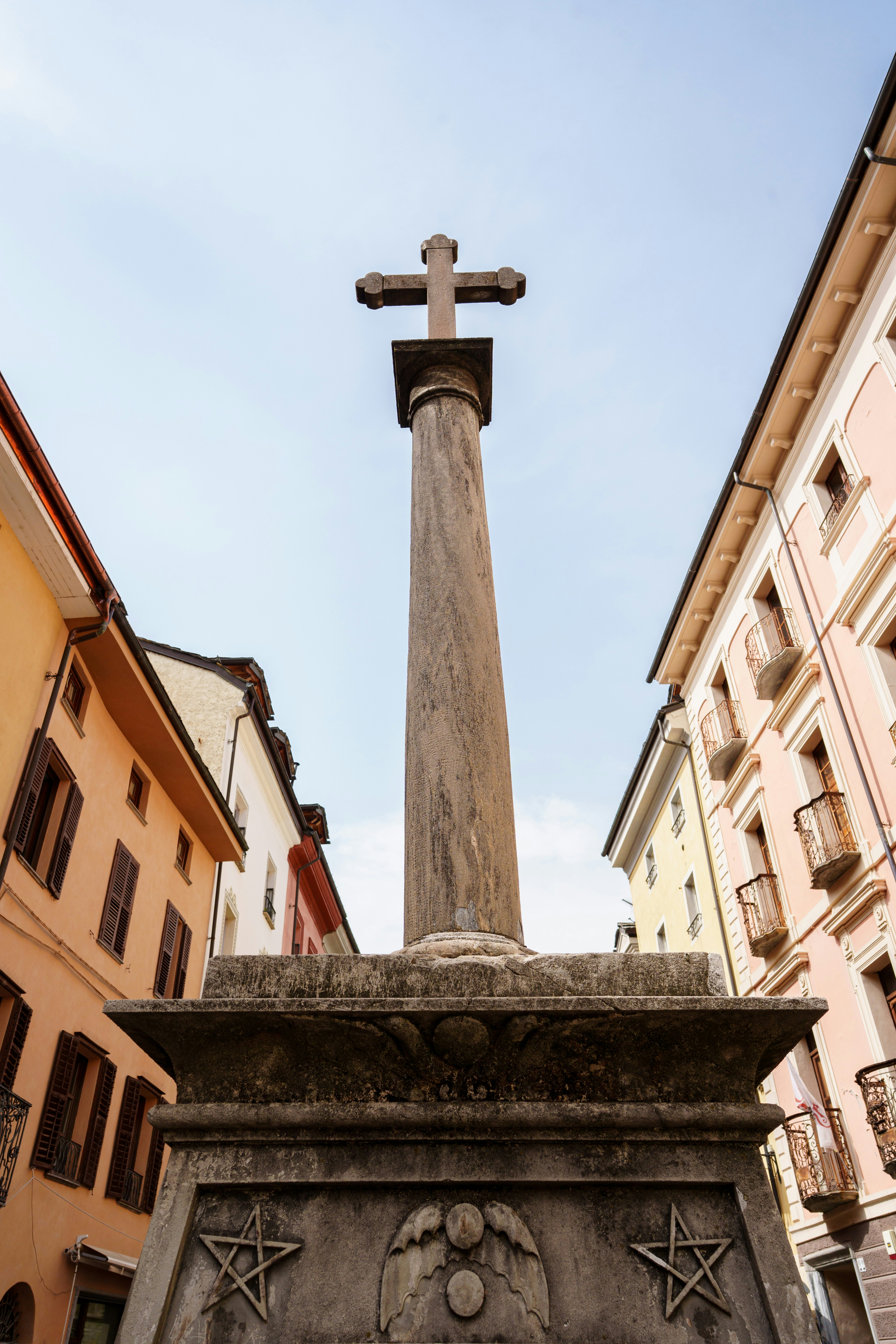 Stone Cross on a City Pillar Framed by Colorful Facades