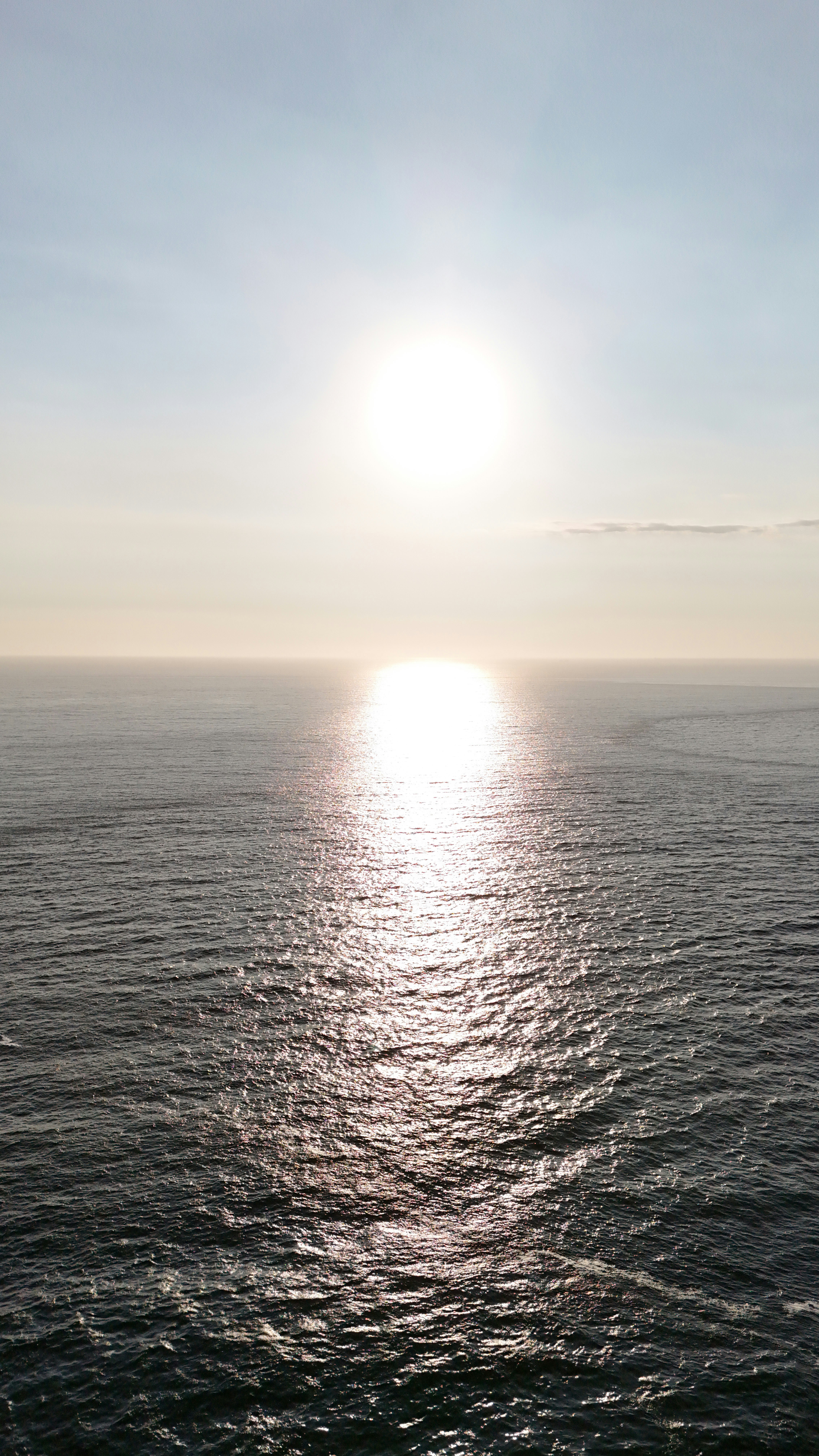 Soft sunrise over a tranquil sea with a bright reflection leading toward the horizon; a serene, wide seascape capturing the glow and rippled water texture. The image is a photography capture of an ocean scene.