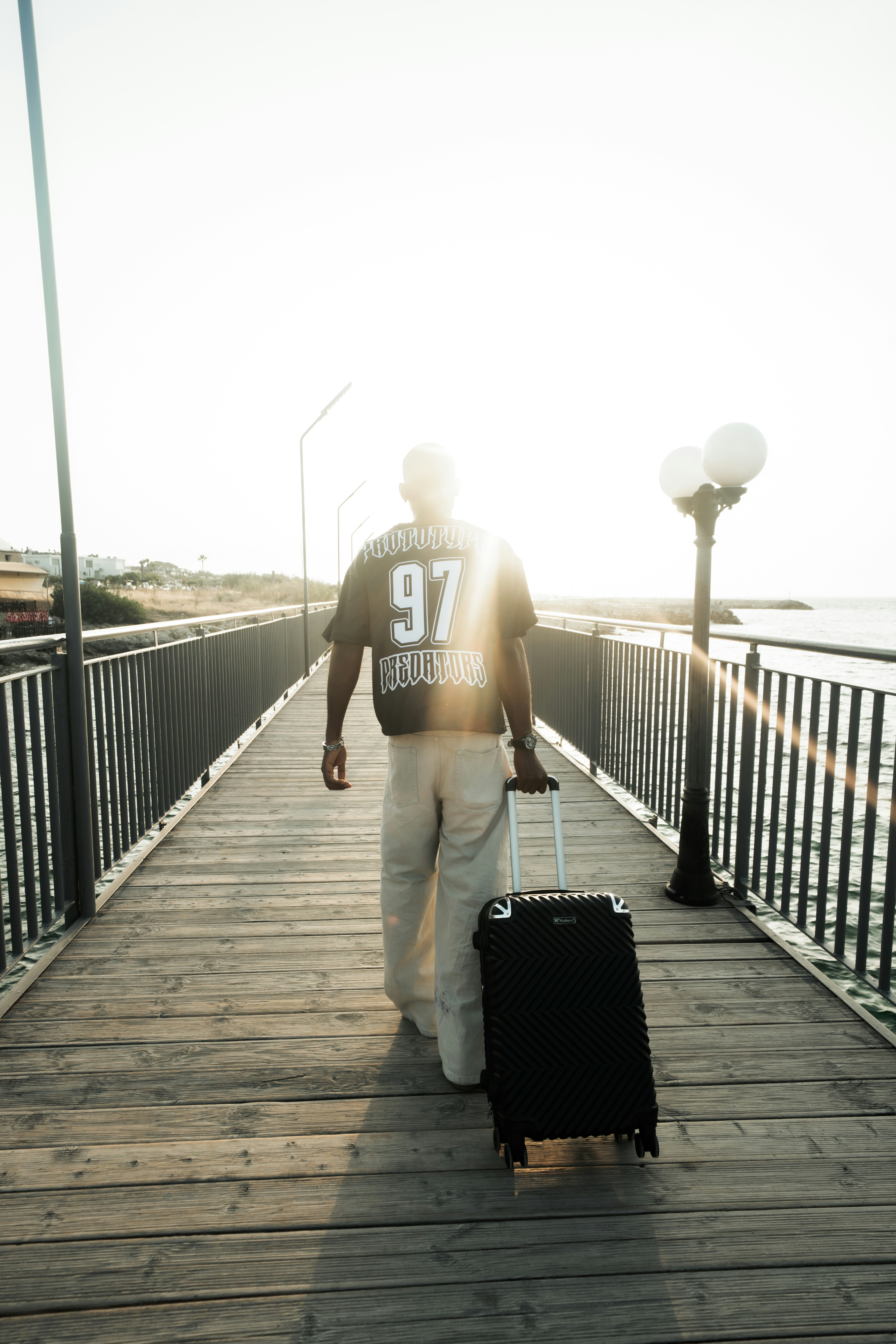 Traveler on a sunlit boardwalk with a rolling suitcase