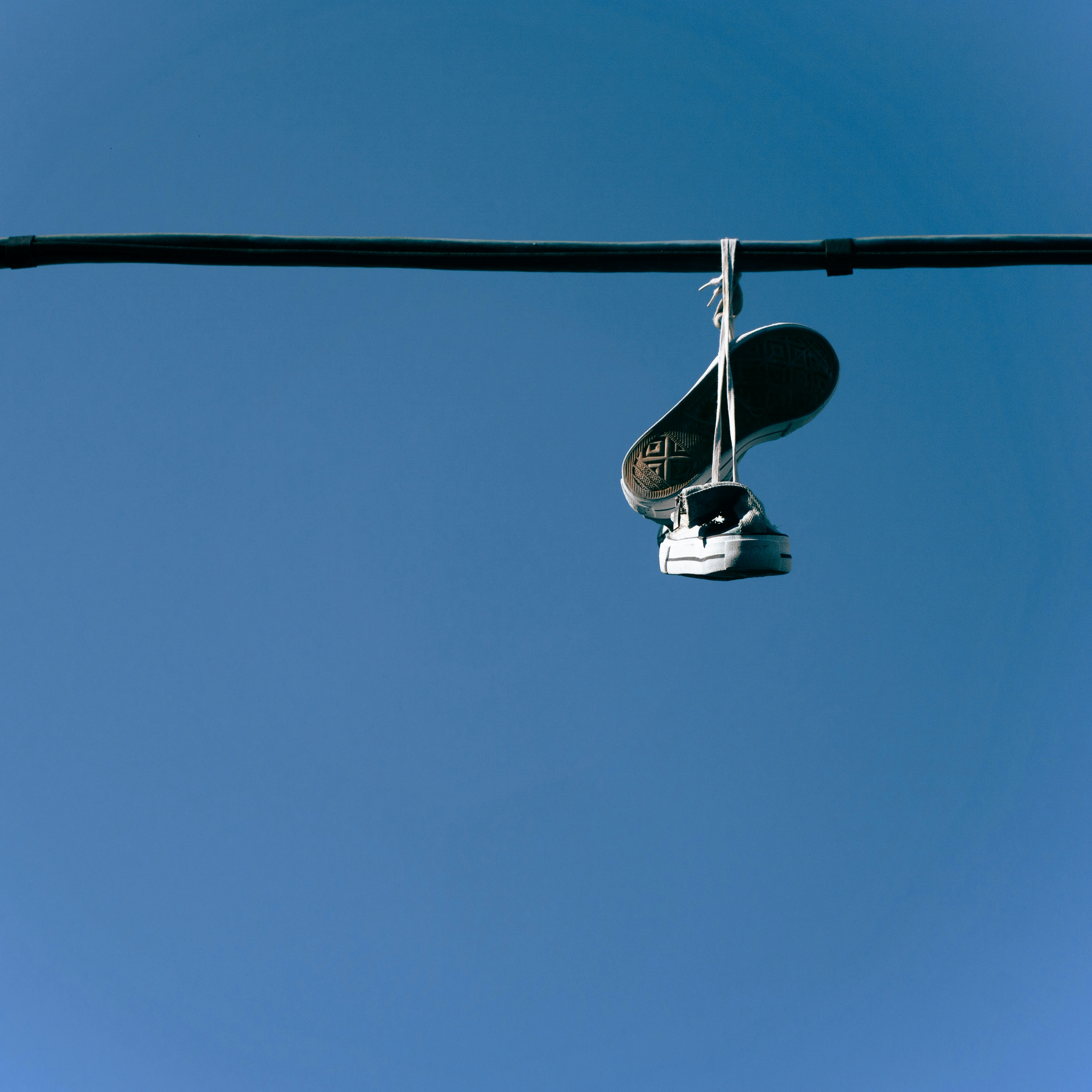 Shoes on a Cable: A Lone Sneaker Against a Clear Blue Sky