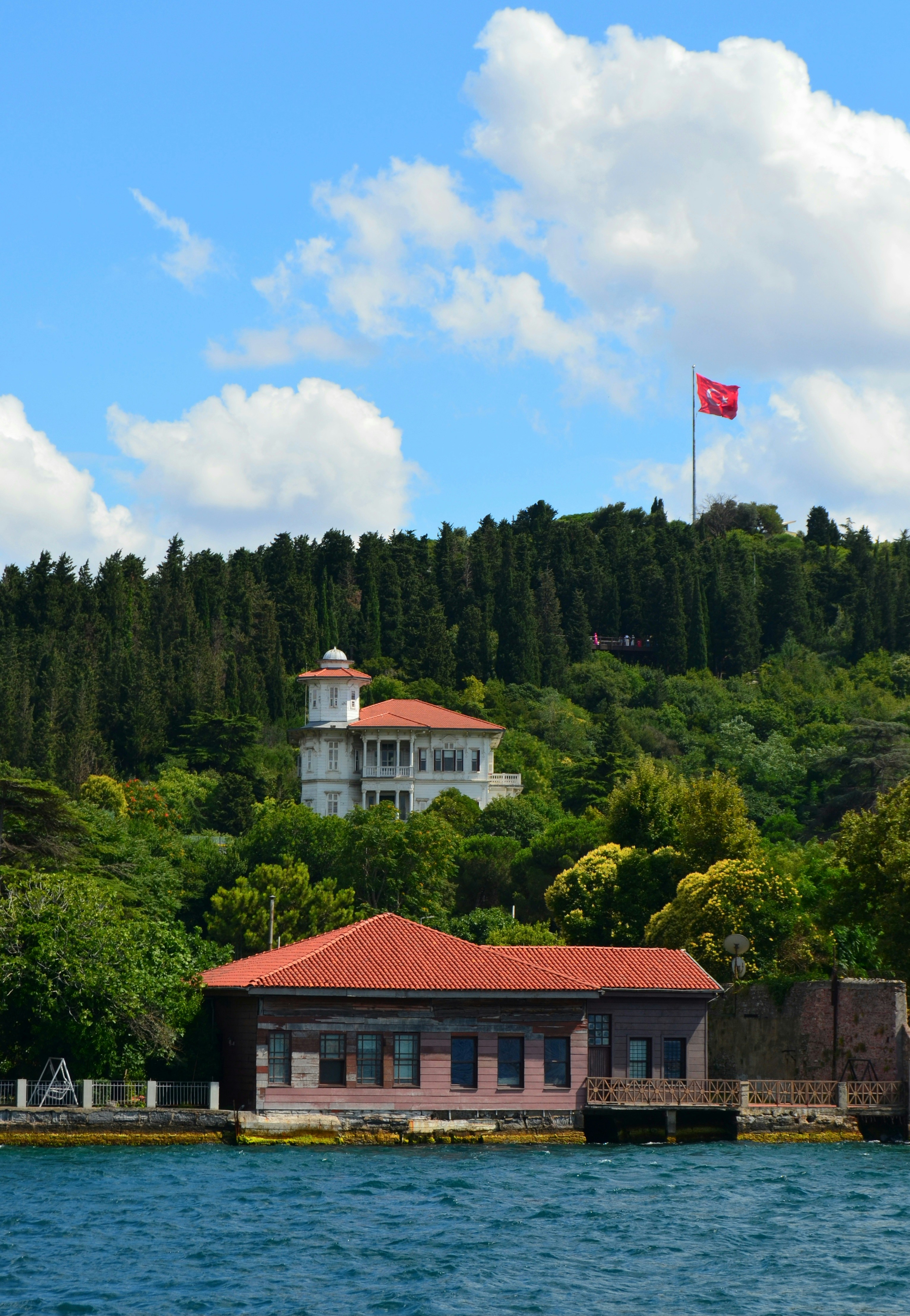 Lakeside villa under a Turkish flag flanked by pine hills