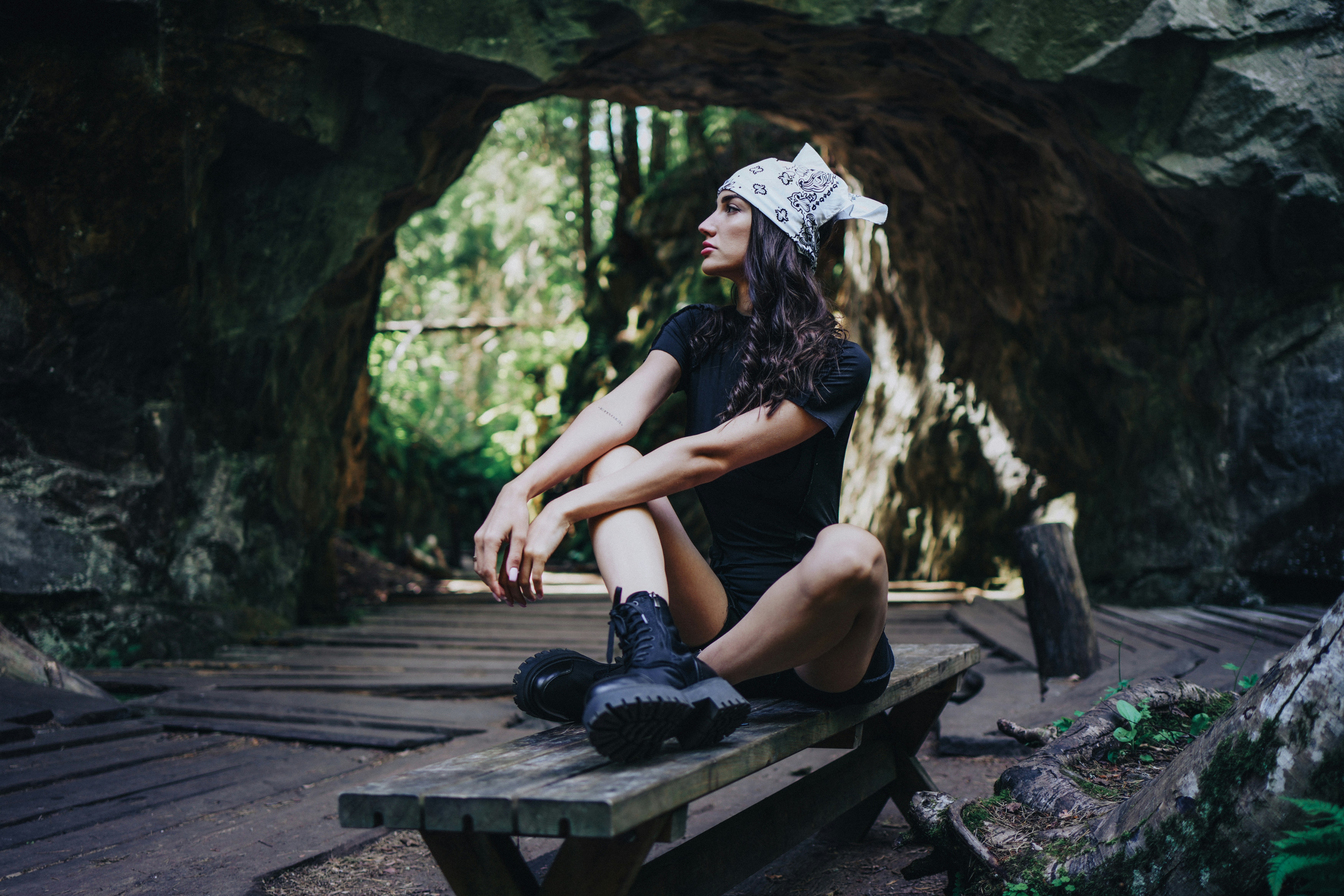 Woman on a wooden bench within a forest cave, contemplative pose under dappled light