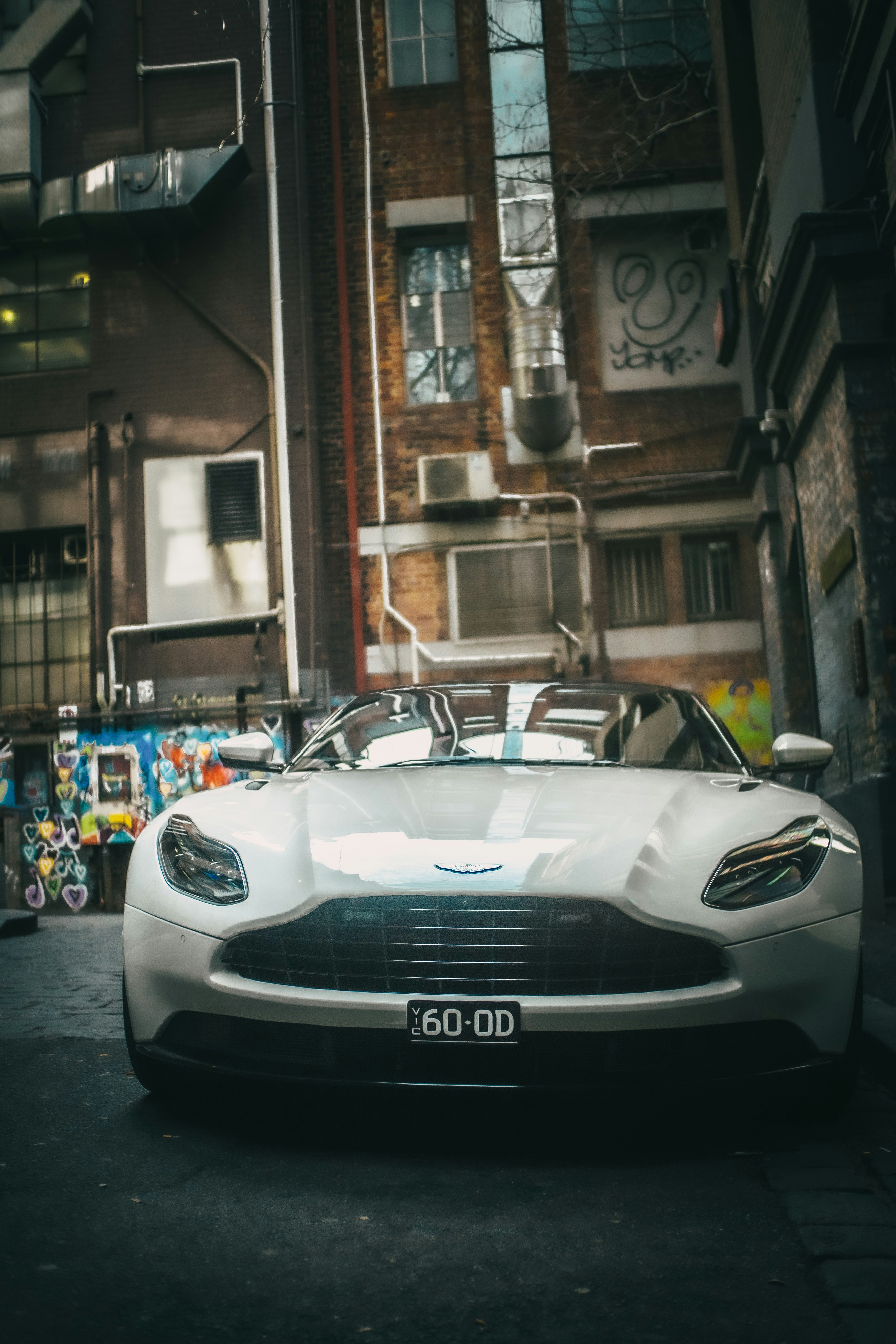 White aston martin sports car parked in a graffiti-covered alley