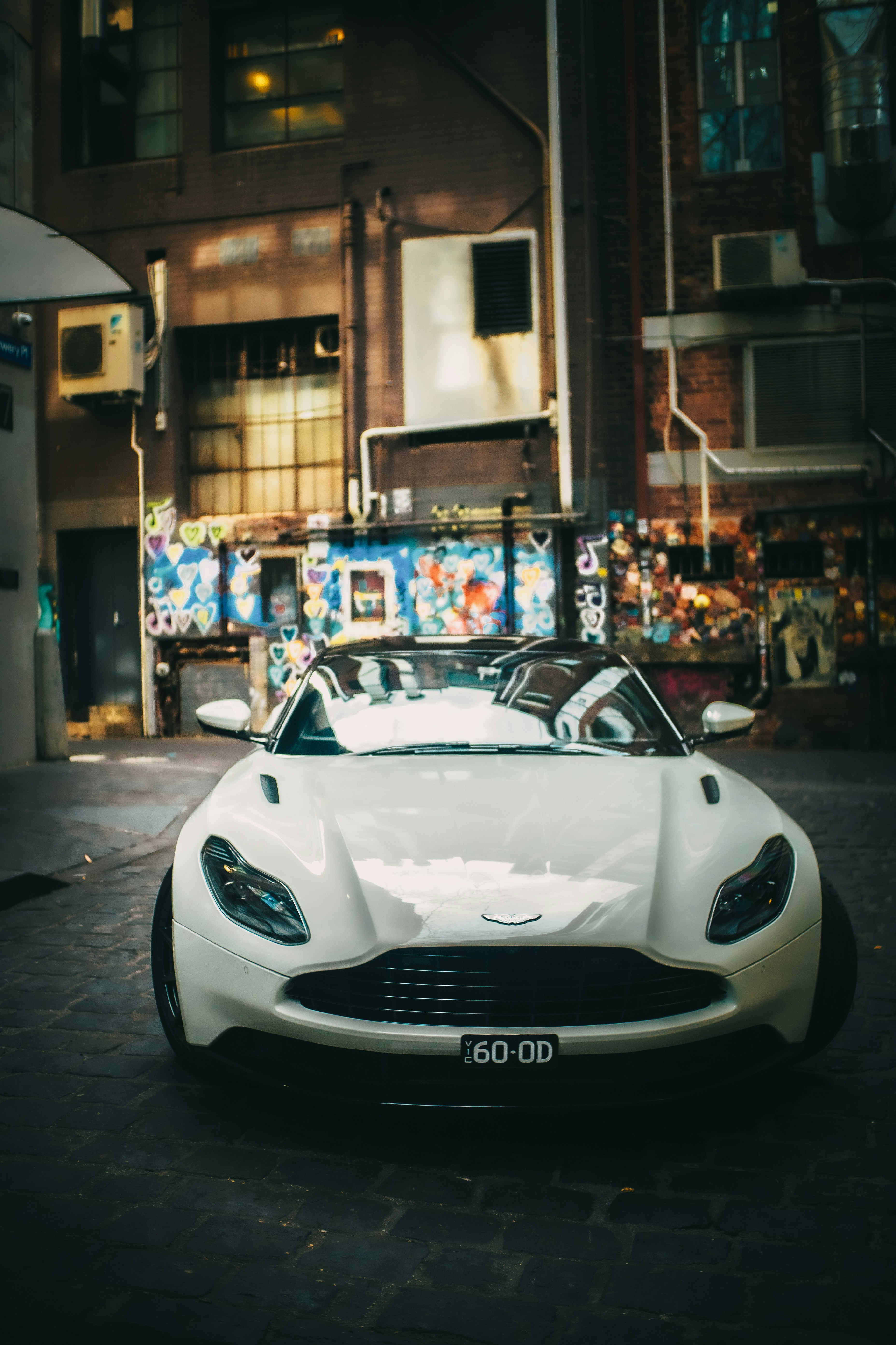 White Aston Martin Halting Street Scene Under Urban mural