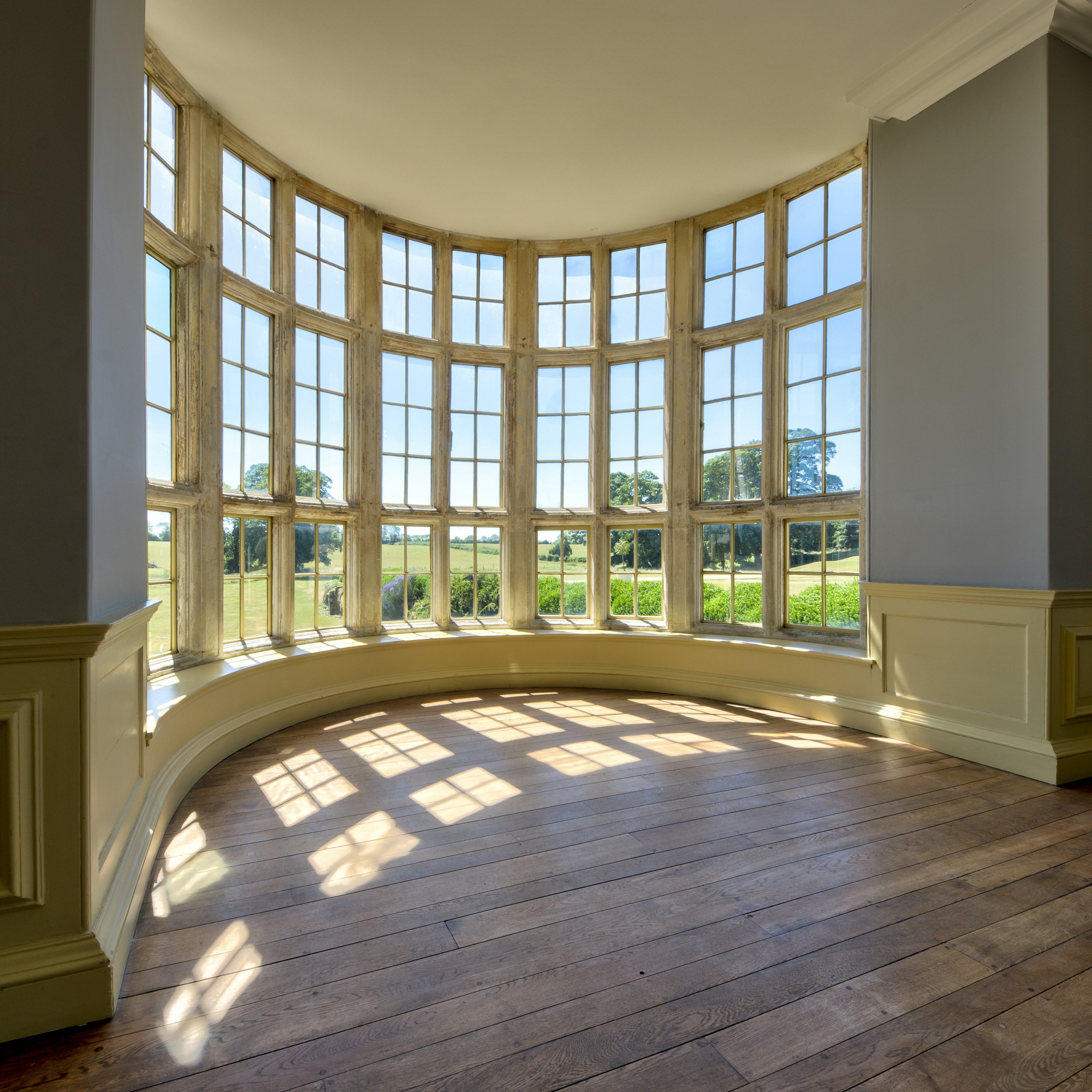 Curved-window sunlit alcove with hardwood curve and pastoral view