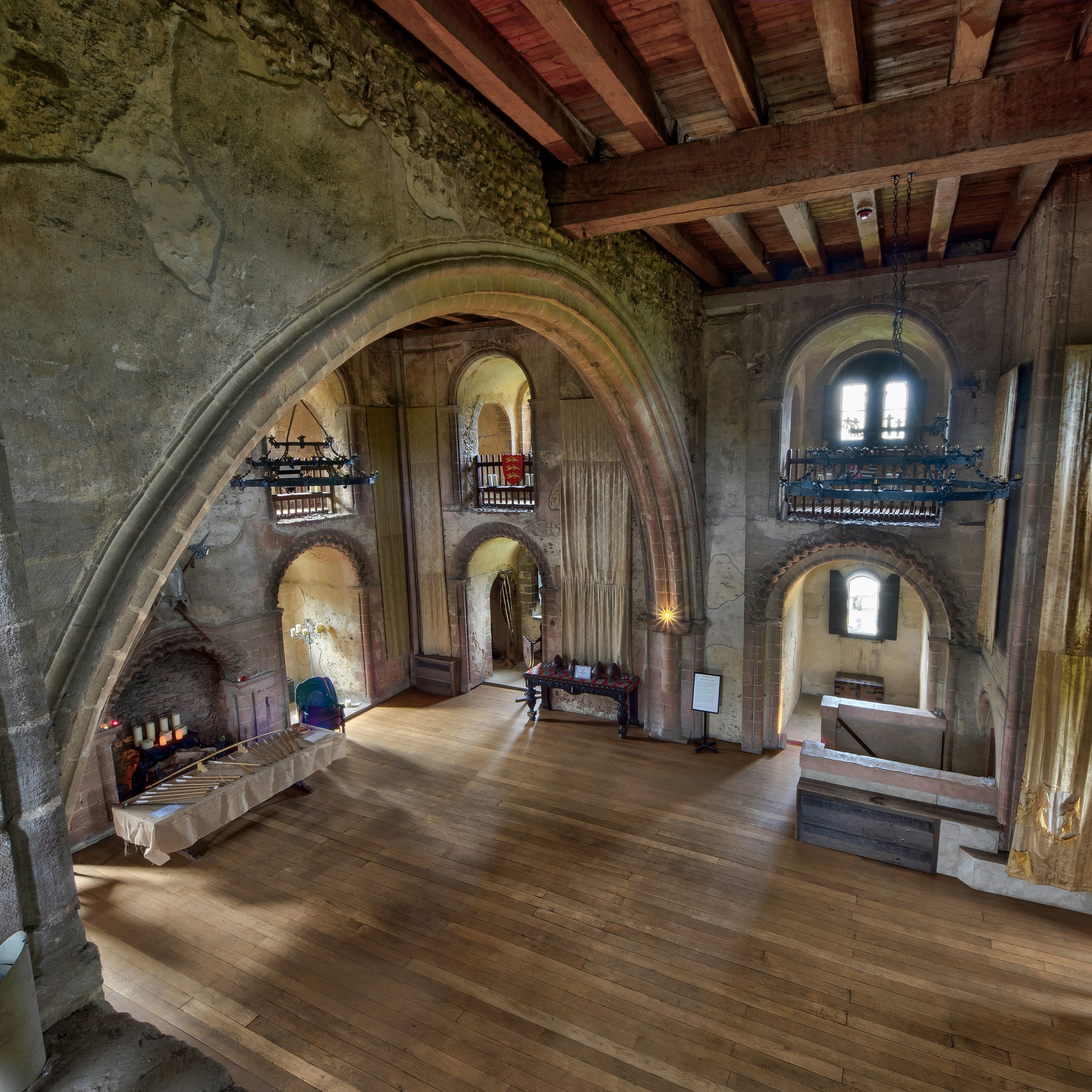 Stone church hall with arches and a wooden floor, warm light streaming through windows; a long table setup on the left and a gallery balcony on the right.