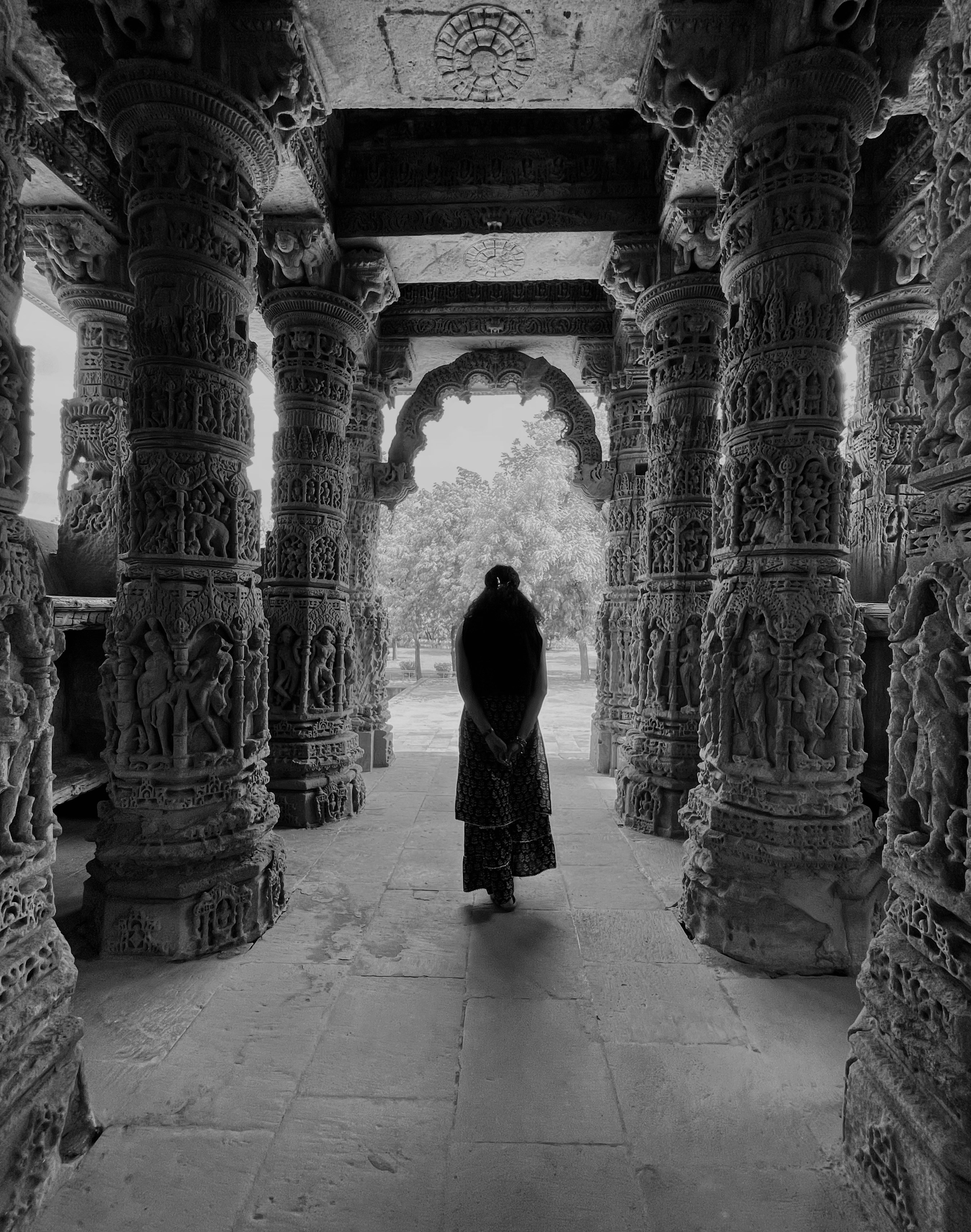 Silhouetted Traveler Beneath Carved Pillars in a Monochrome Corridor