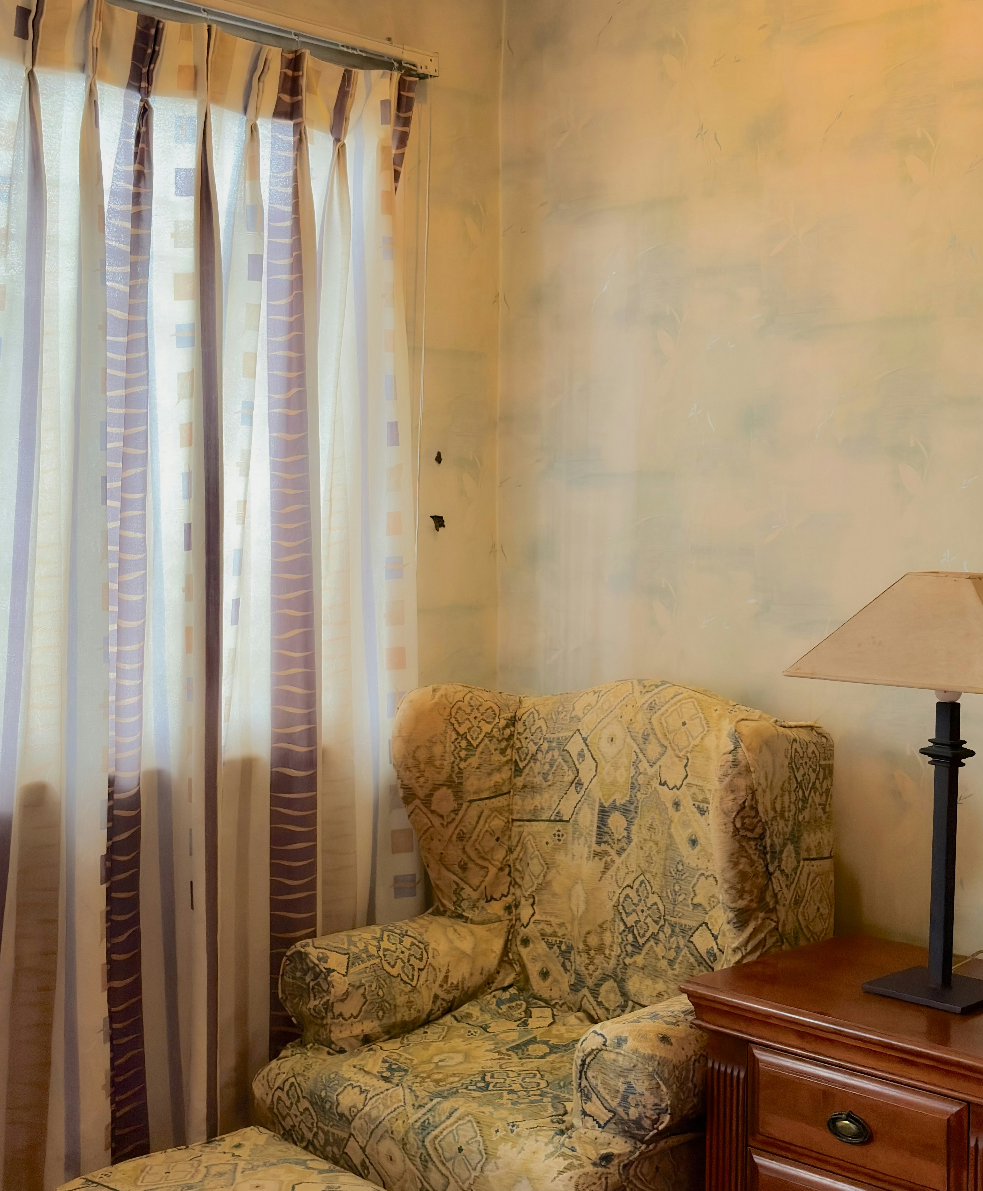 Muted living room sanctuary: patterned chair, lamp, and sheer curtains