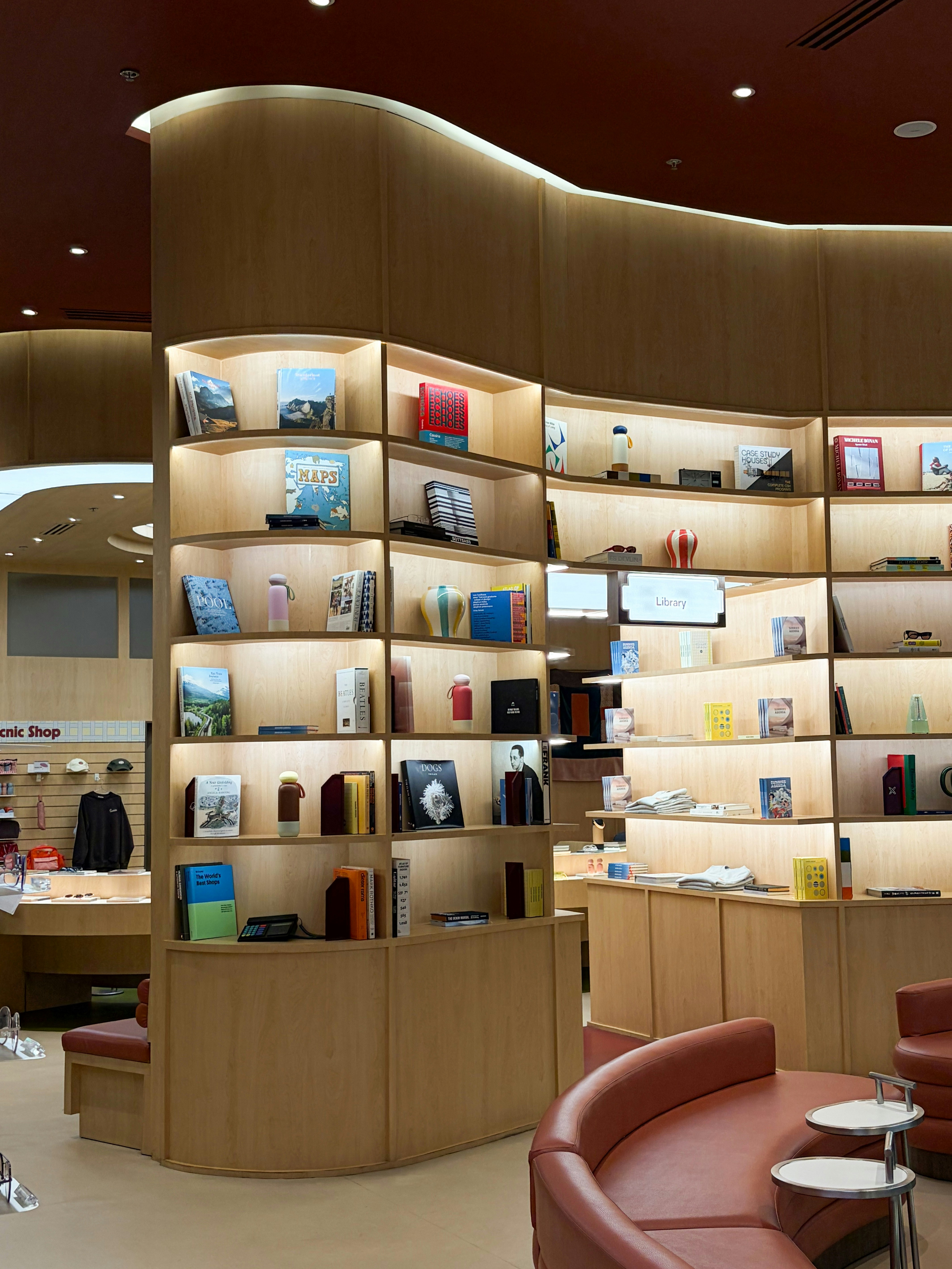 Curved wooden shelves filled with books in a softly lit library space, with red leather seating in the foreground.