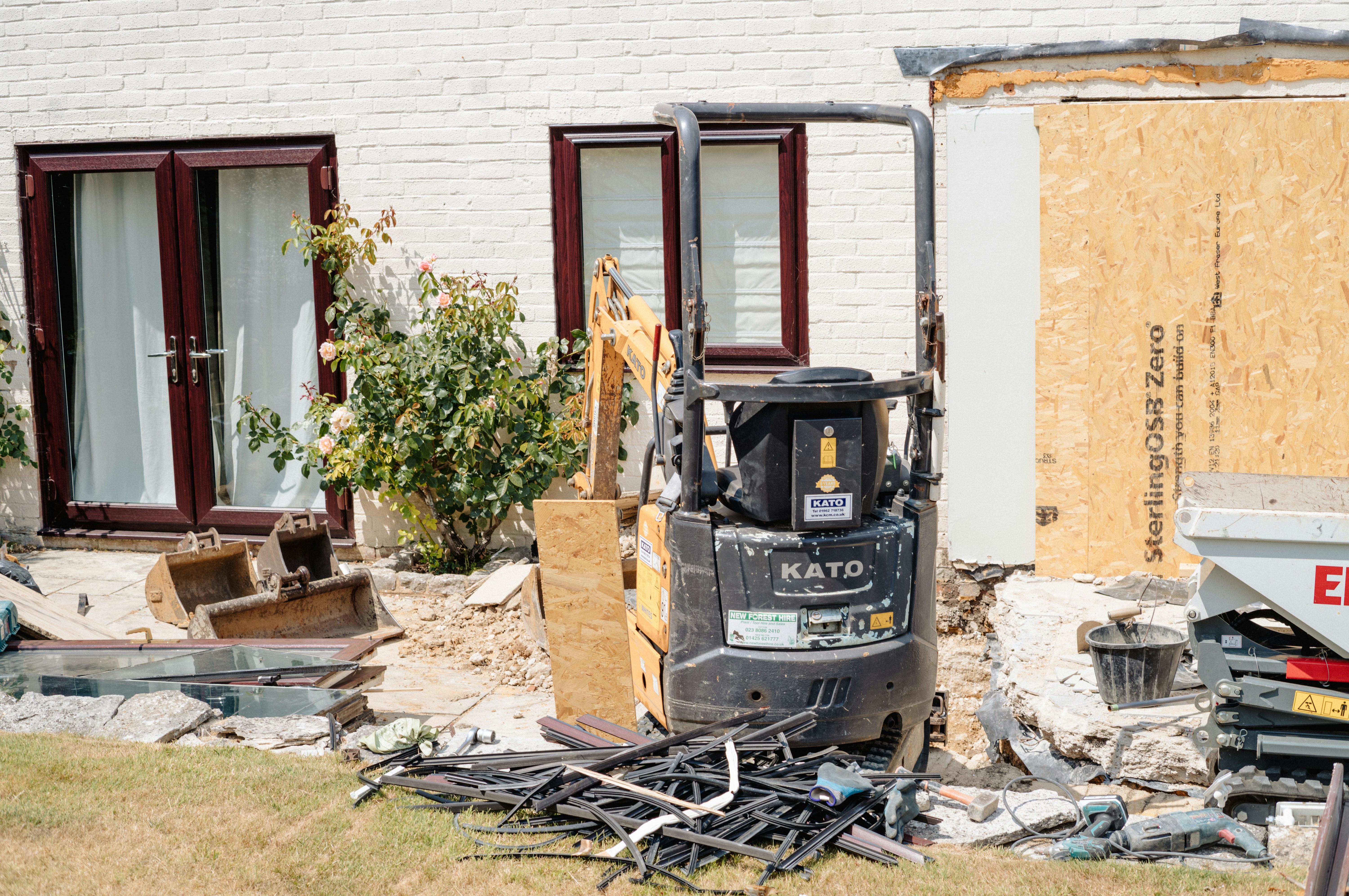 Construction Scene with Excavator Amid Debris in Front of a Partially Renovated House