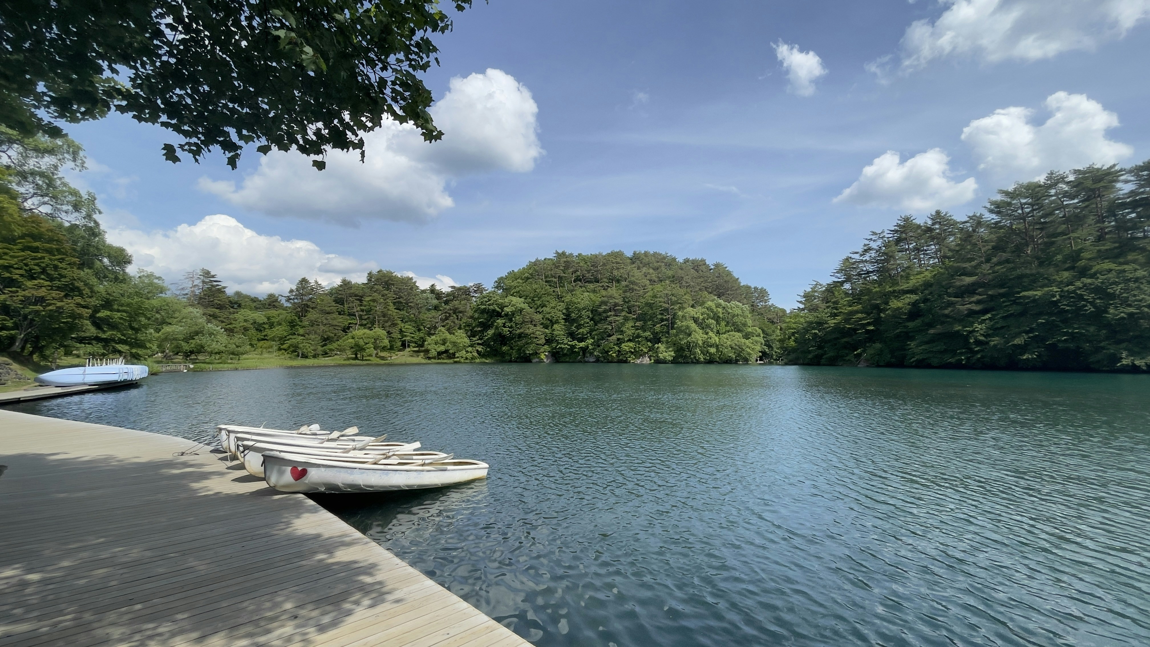 Calm lake with small boats docked along a sandy shore under a bright, partly cloudy sky.