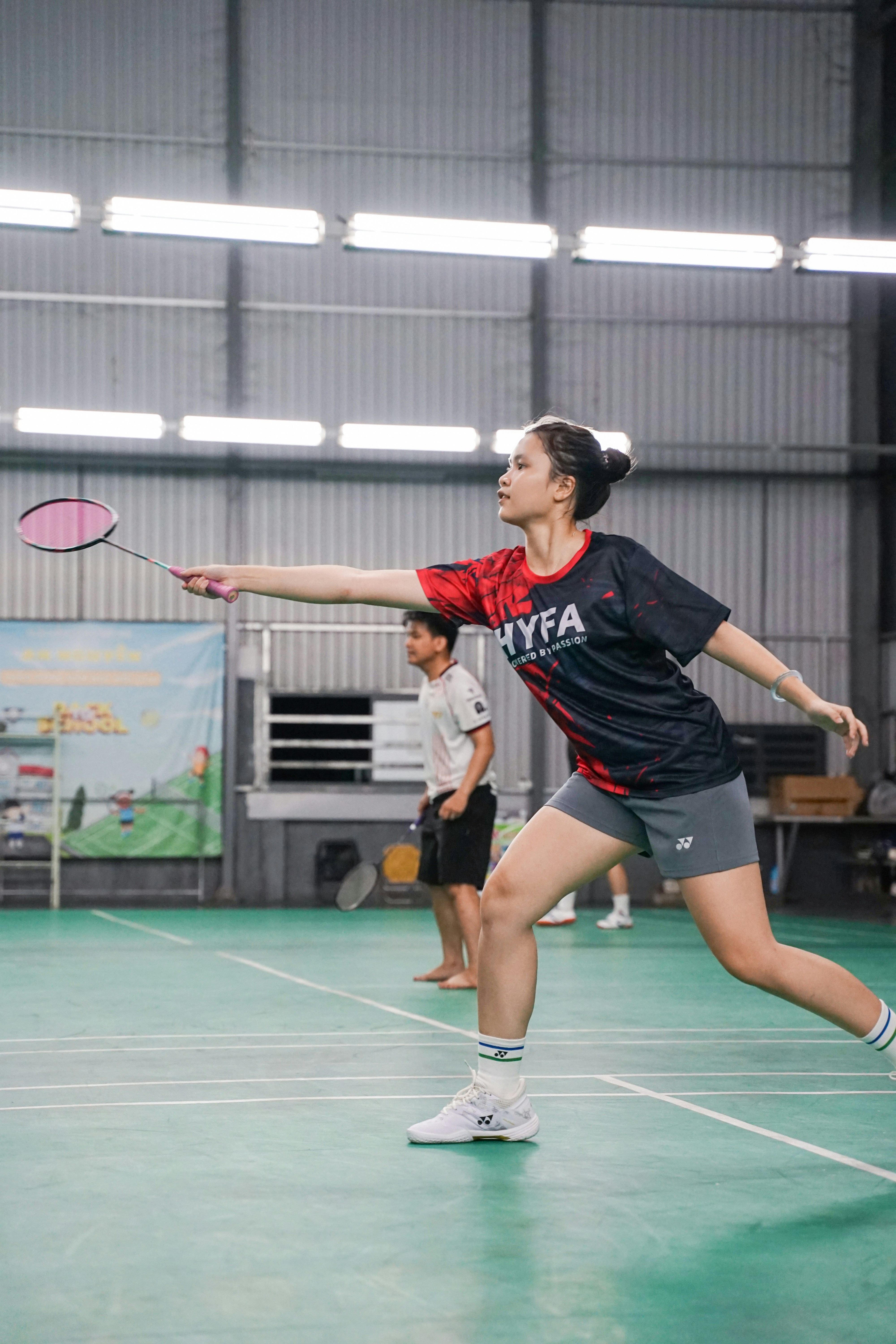 Lunge and reach: a badminton player in mid-serve on a gym court