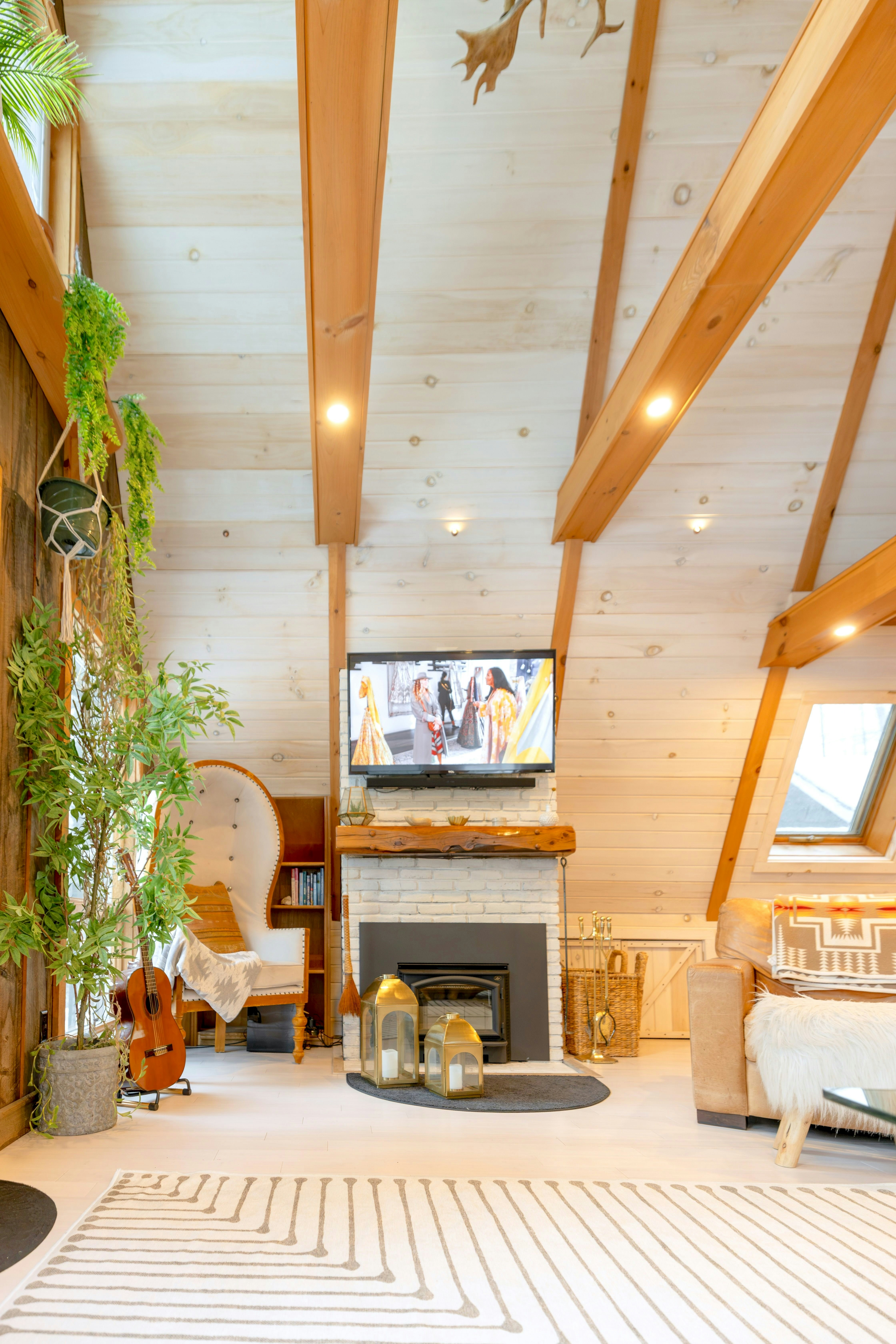 Bright loft living room with a stone fireplace, hanging TV, guitar, plants, and a striped rug.