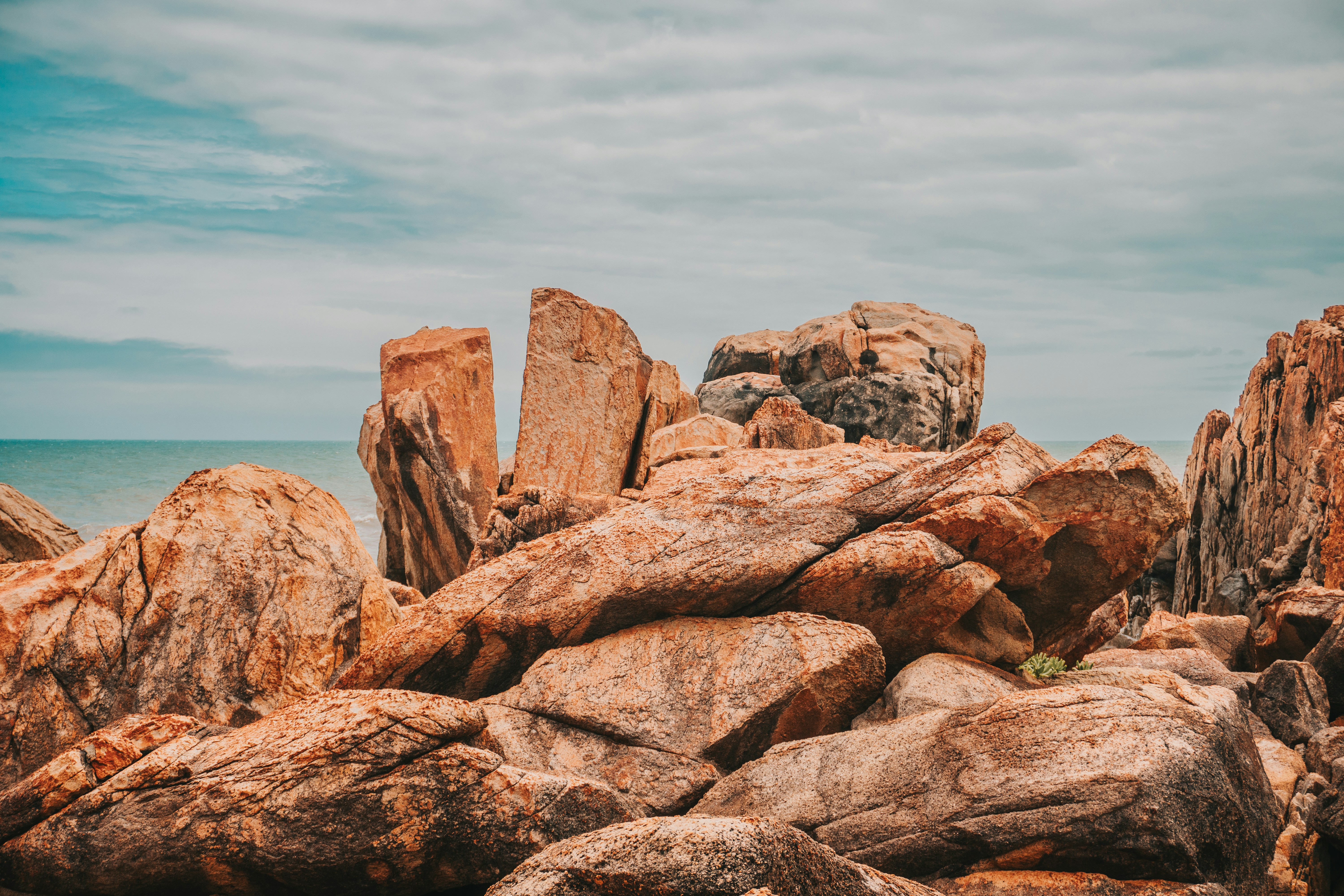 Rugged coastline with weathered granite boulders by a calm sea under a soft, cloudy sky.