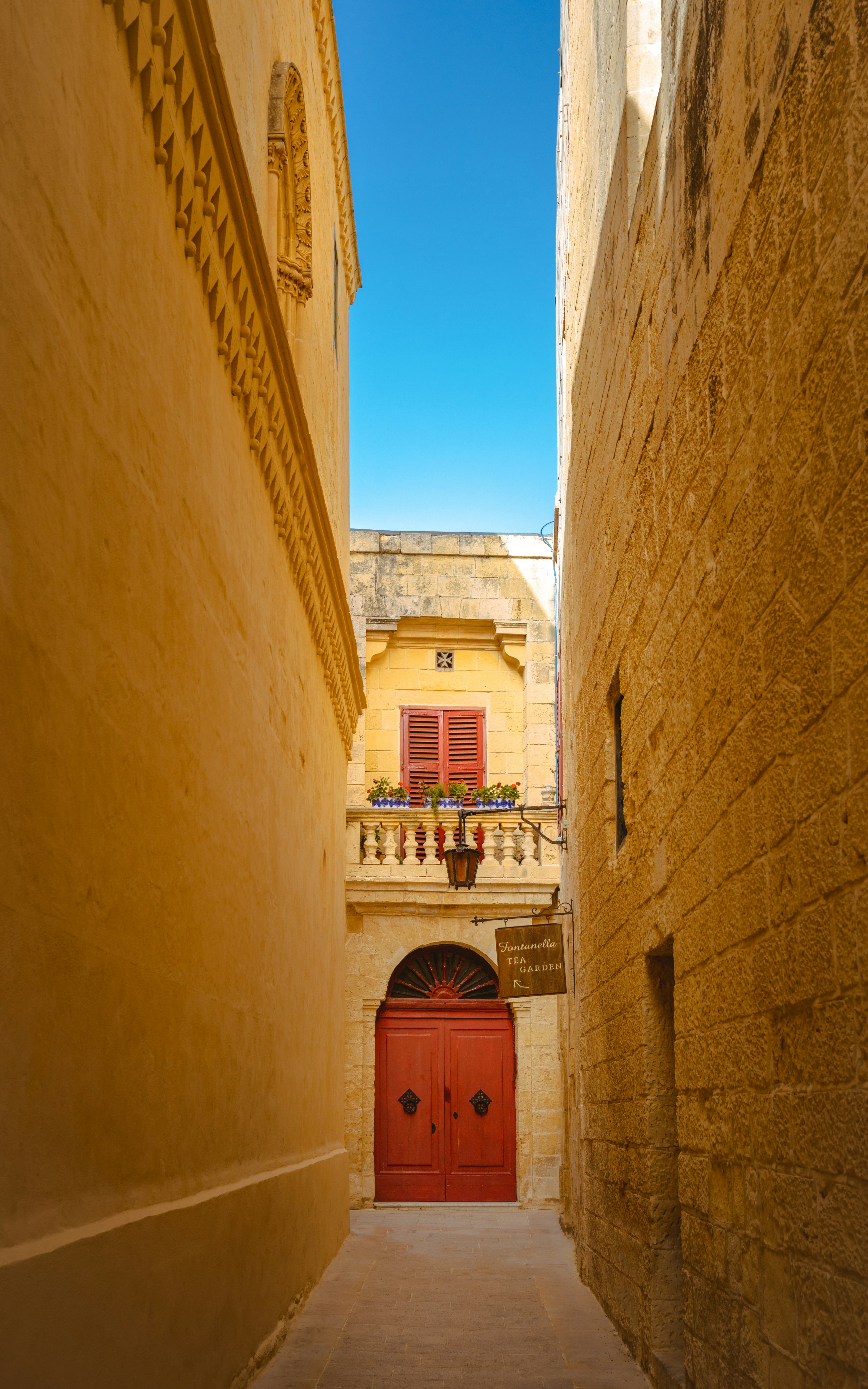 RedDoor Alley: A Sunlit Passage Between Warm Limestone Walls