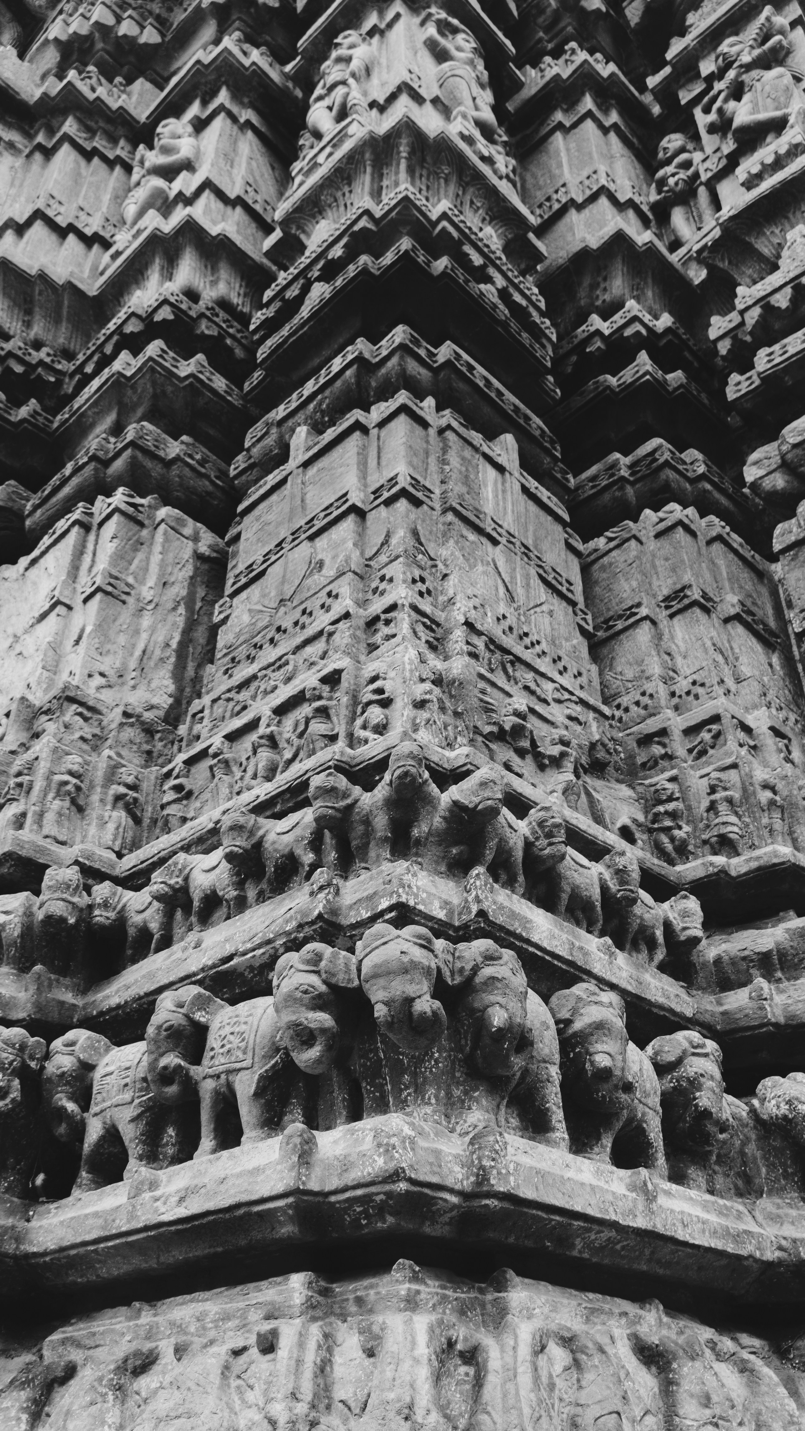 A dramatic black and white vertical view of intricately carved ancient temple architecture. Intricate stone friezes depicting elephants and deities layer upward in striking geometric relief, highlighting centuries of fine craft and timeless sculpture.