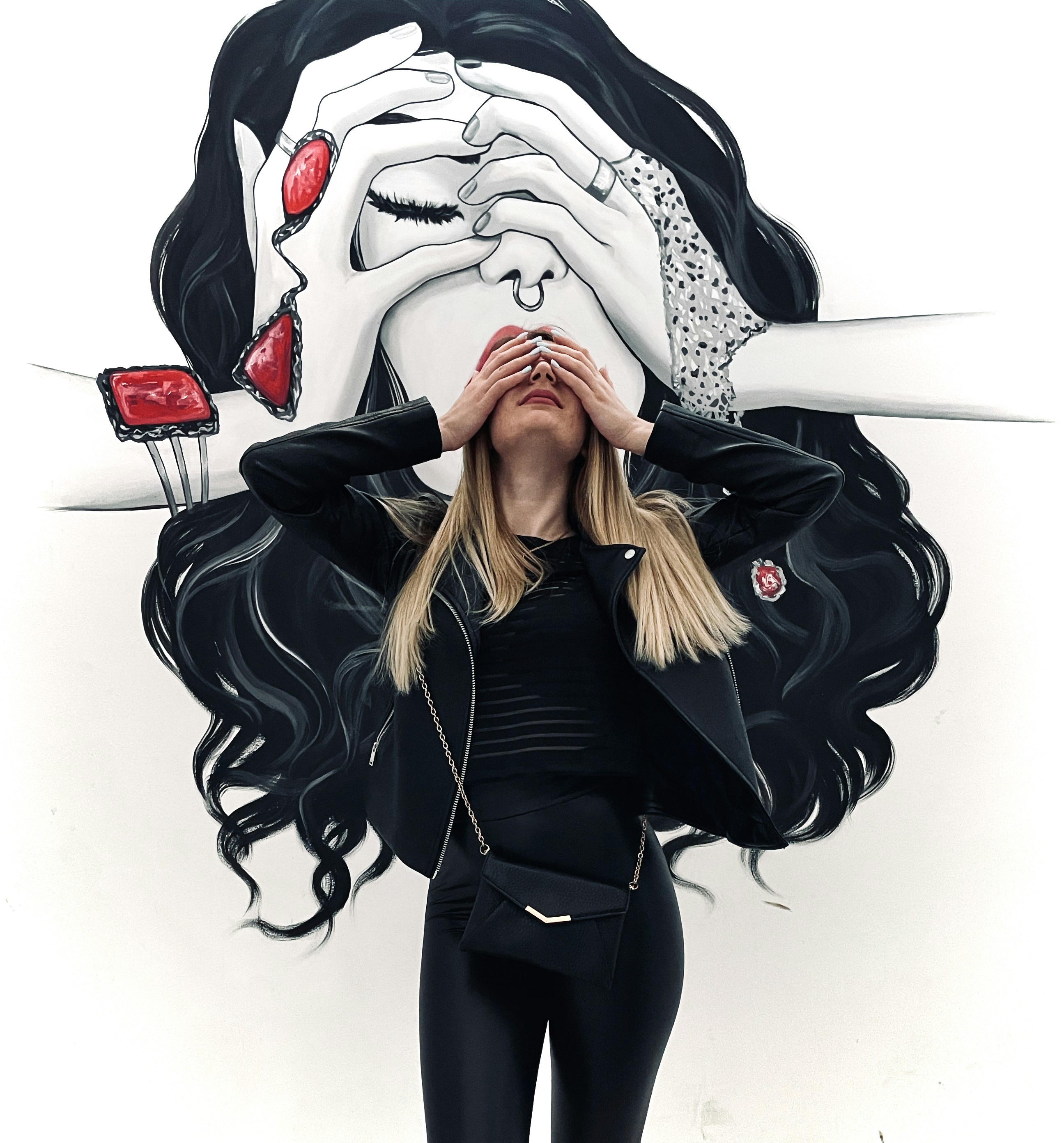 Masked Reverie: A Woman in Black Stands Before a Surreal Wall Portrait