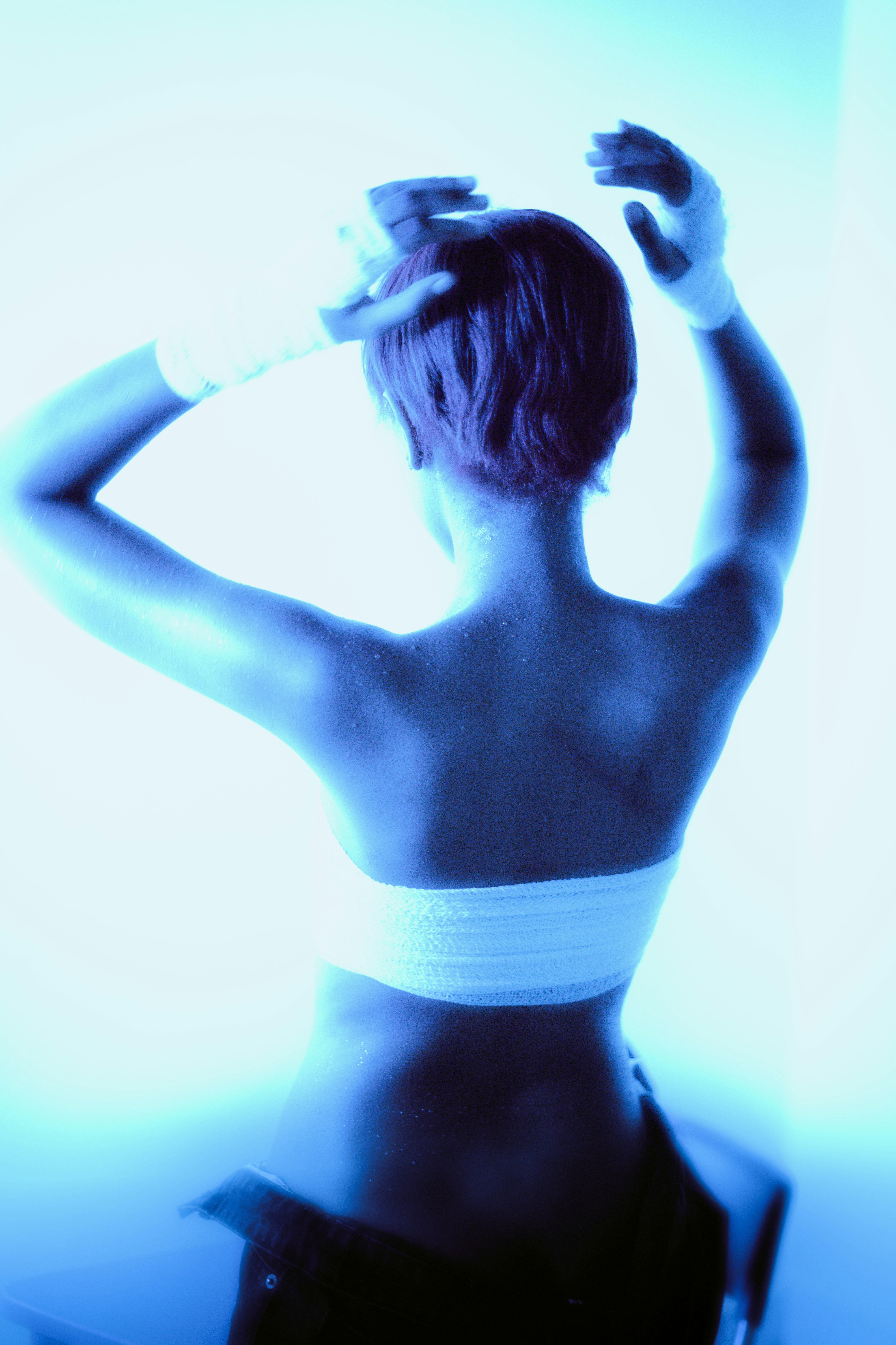 Blue-tinted silhouette: back view of a dancer raising arms in an acrylic glow
