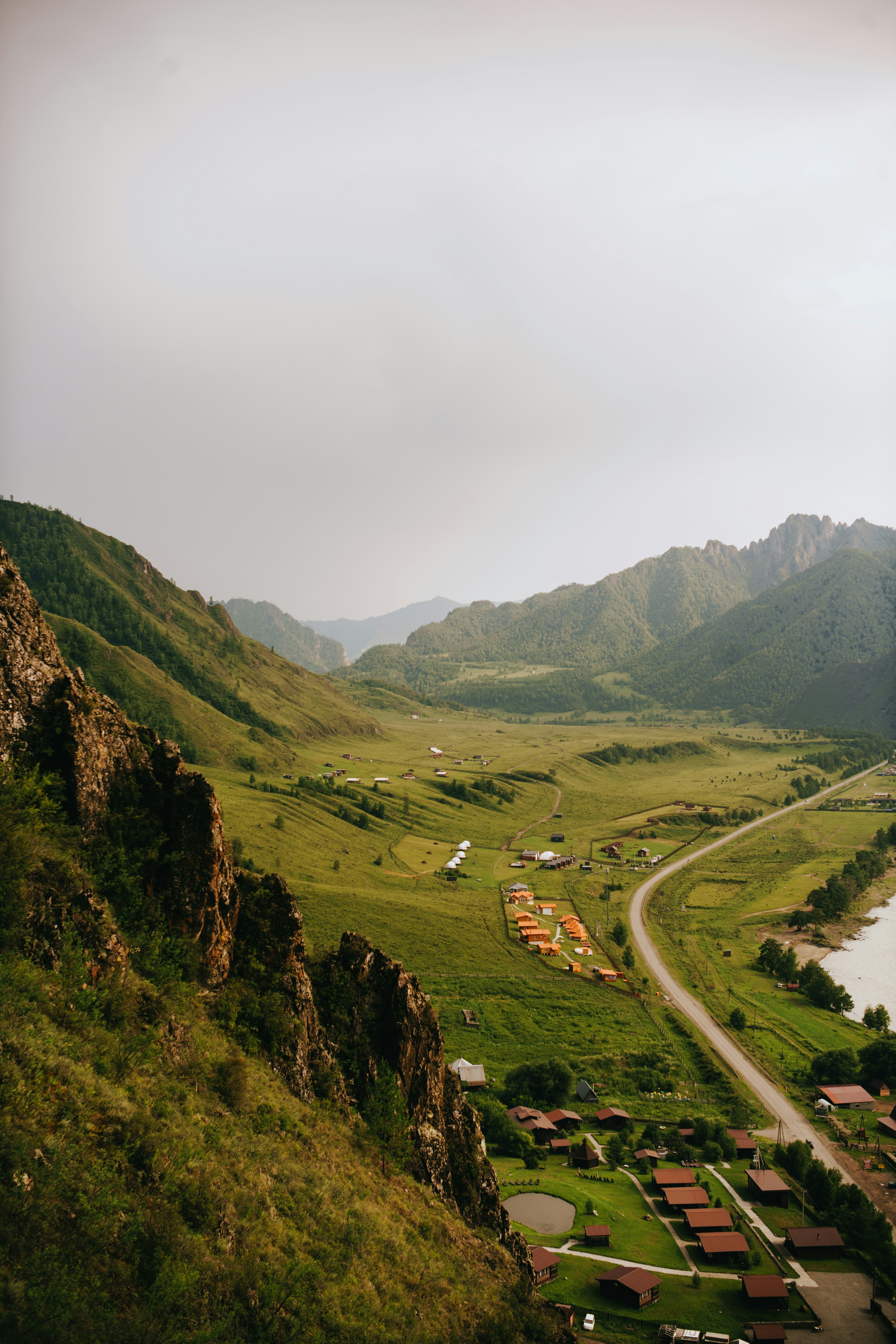 Rolling green valley with winding road and a cluster of red-roofed houses nestled between rugged cliffs and distant hills.