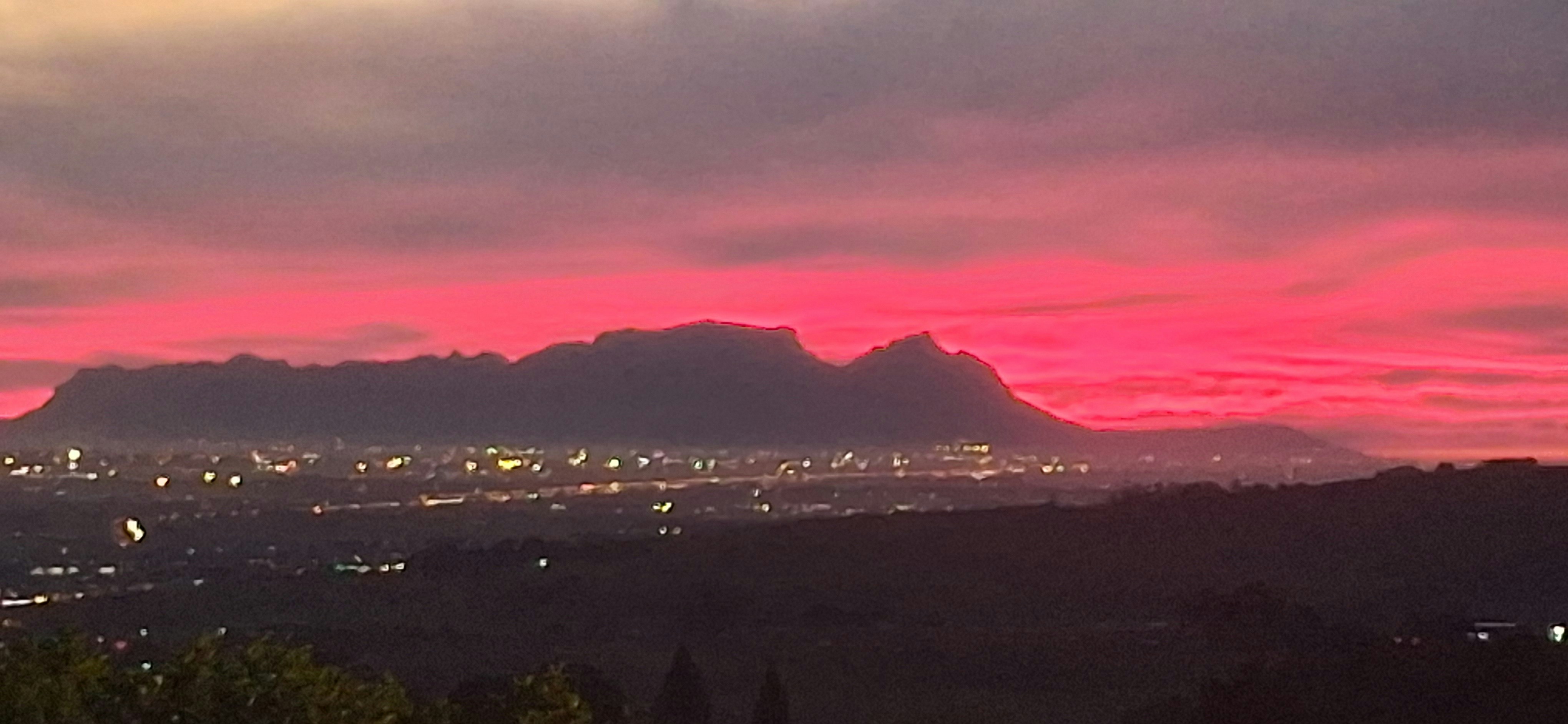 Crimson Dusk Over the Valley: A Town Light Pinpricks Beneath a Rugged Horizon