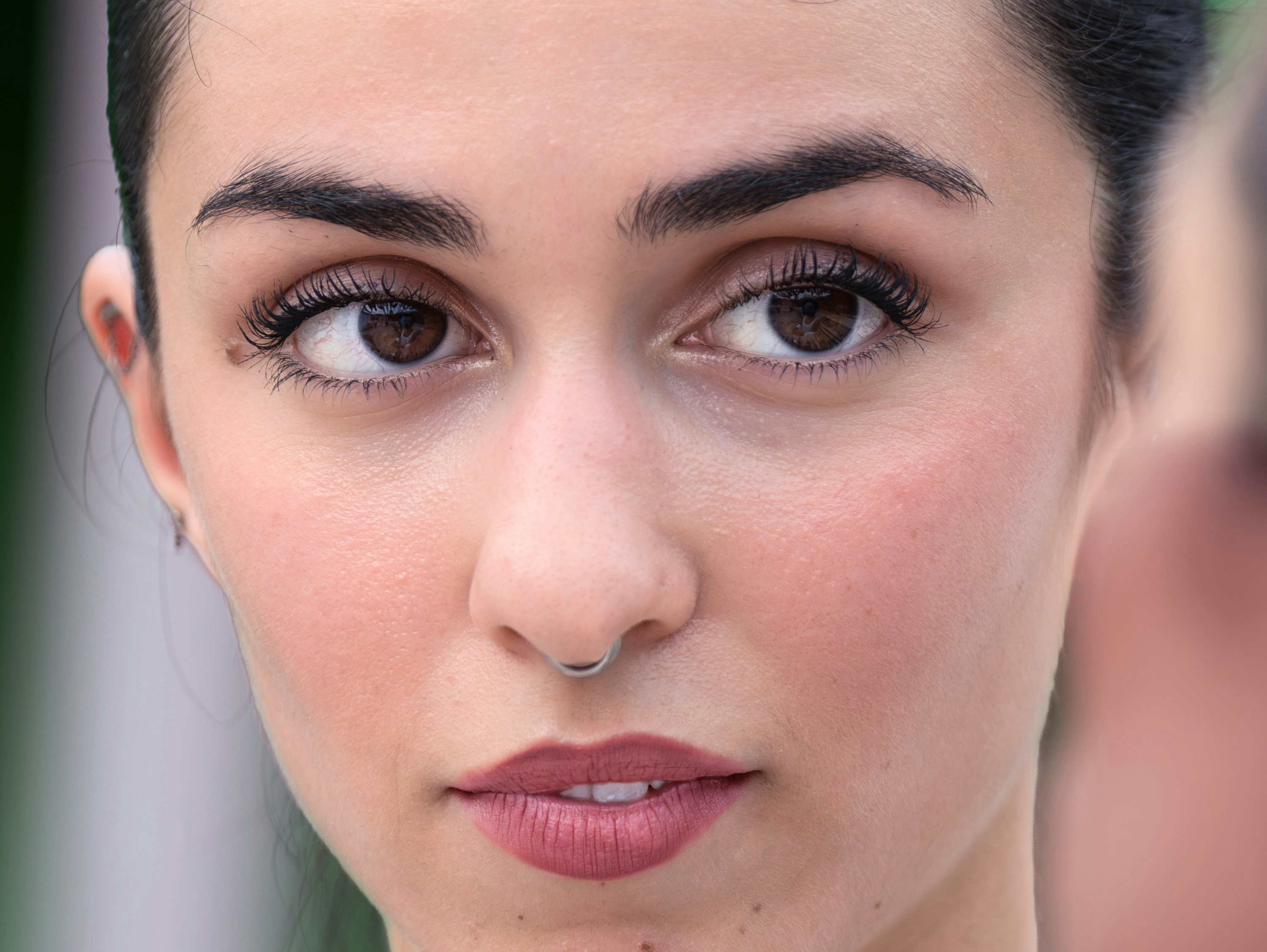Close-up portrait of a woman with a calm gaze, showing flawless skin tones and subtle makeup; the image emphasizes facial features and expression with a blurred background.