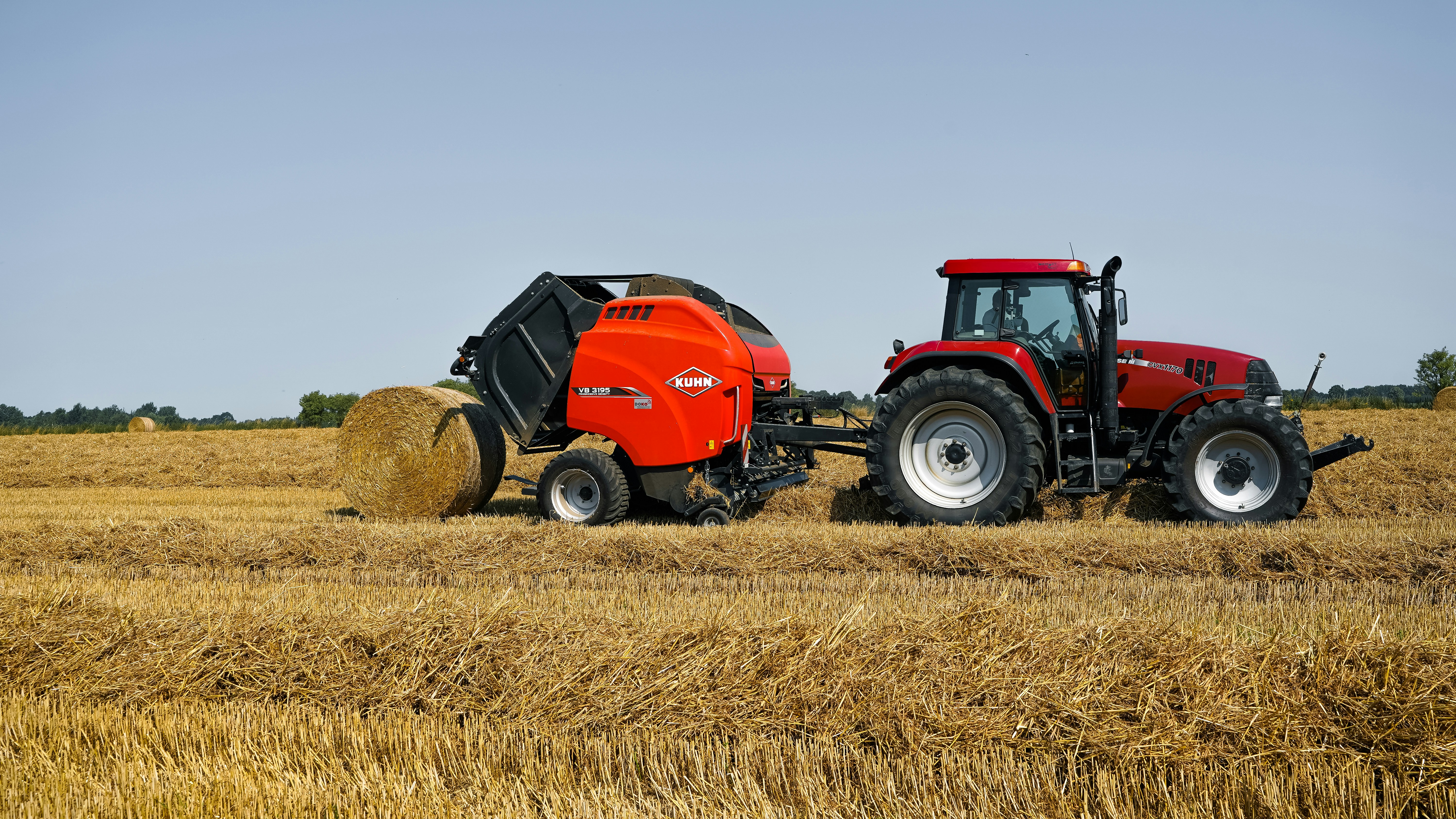 Red Tractor at Work: Harvest Field Under a Clear Sky