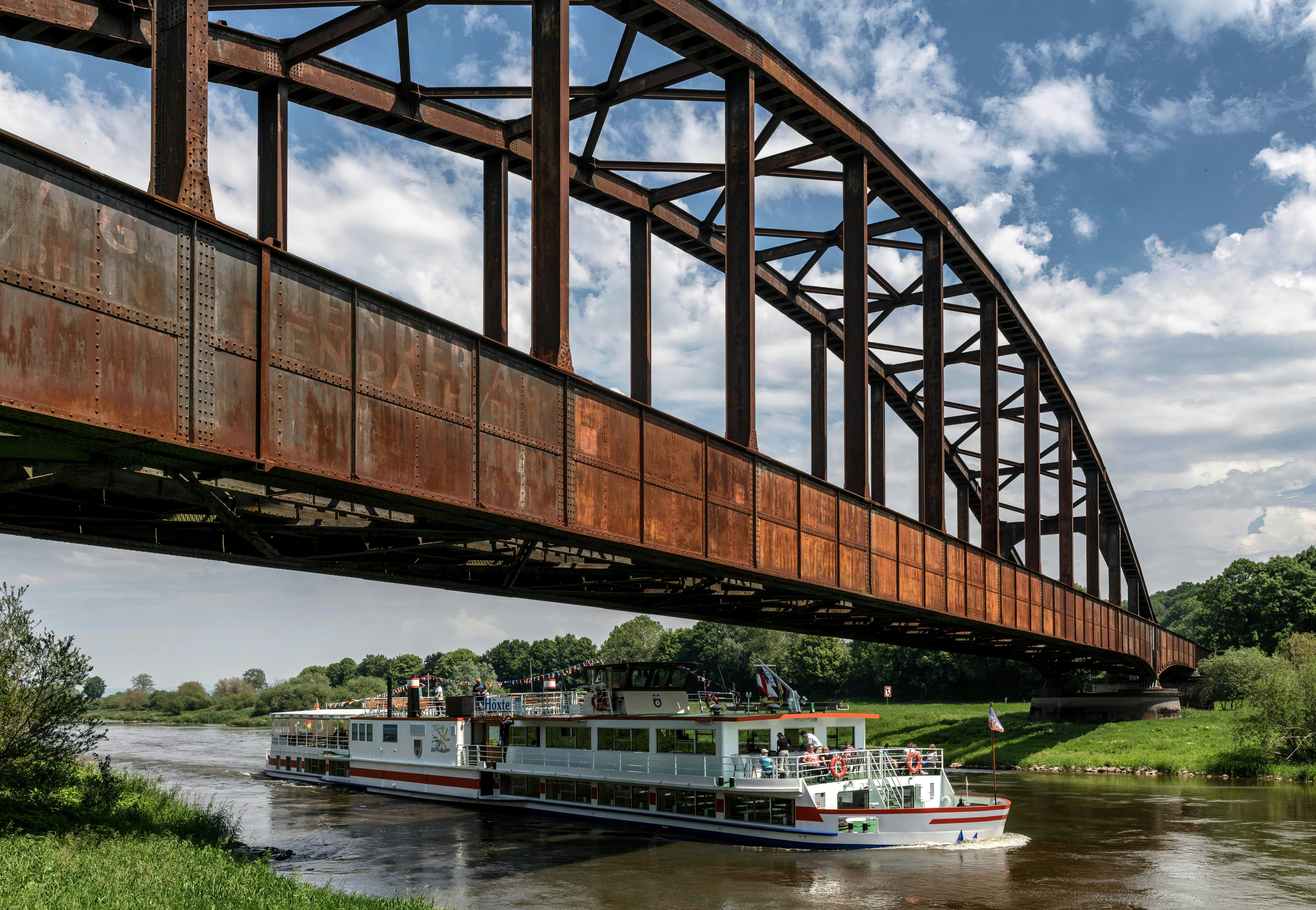 Rusted Arch Over the Waterway: A Riverboat Glide Beneath Steel Trusses